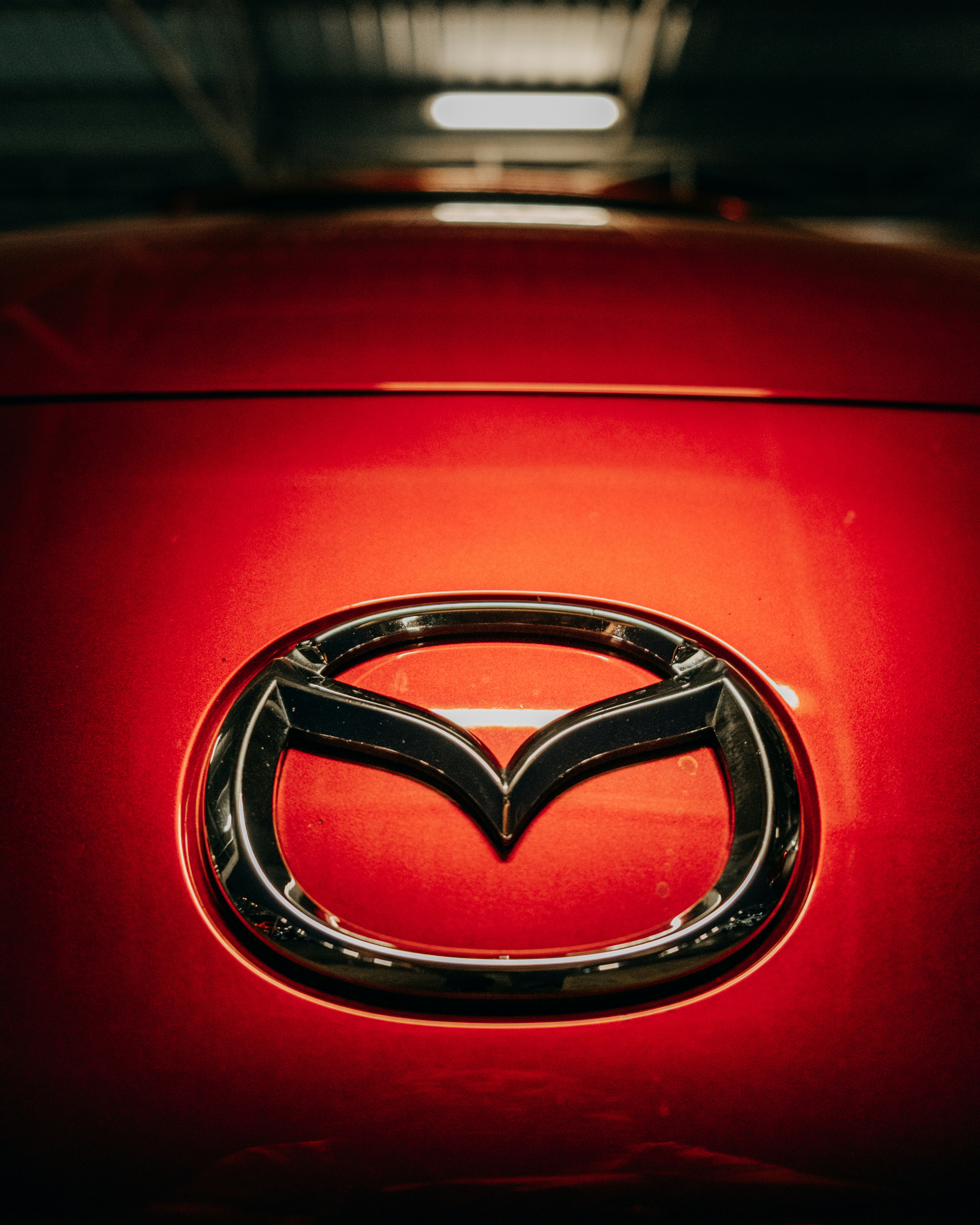 Red Emblem, Dark Reflection: Mazda Badge Bathed in Industrial Glow