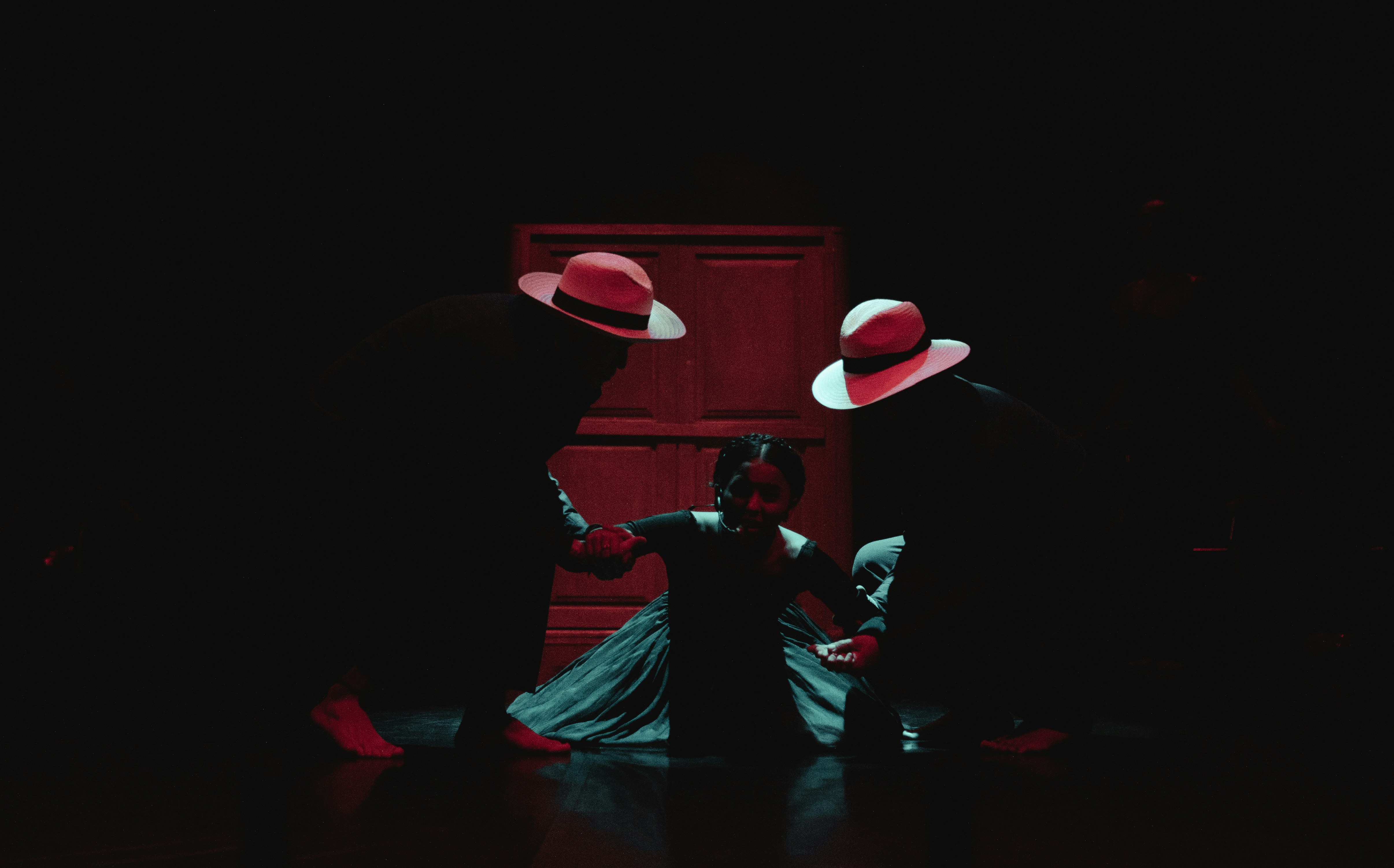 Red-Hatted silhouettes cradle a dancer in a shadowed stage
