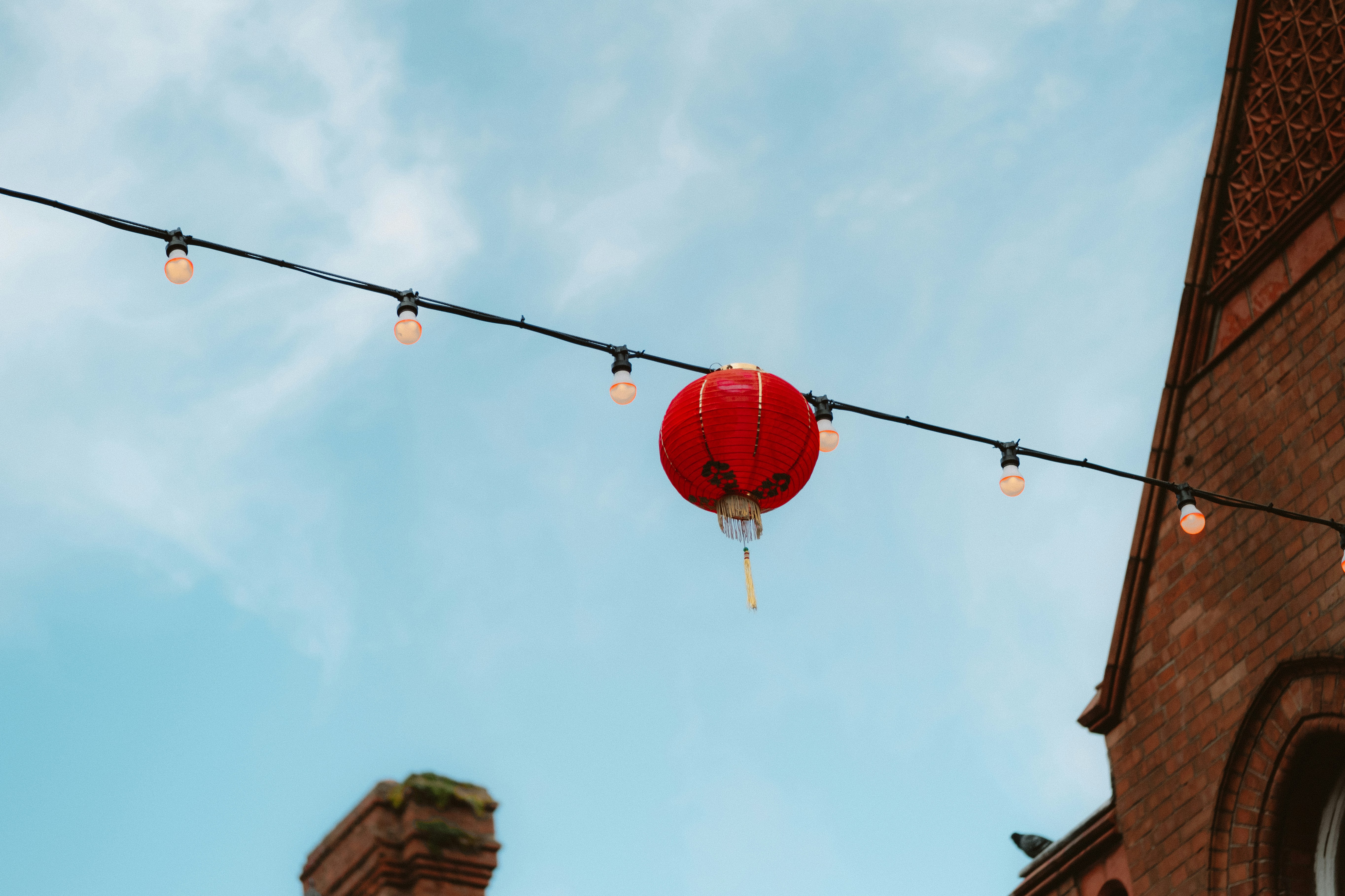 Red Lantern Under a String of Lights Against a Bright Blue Sky