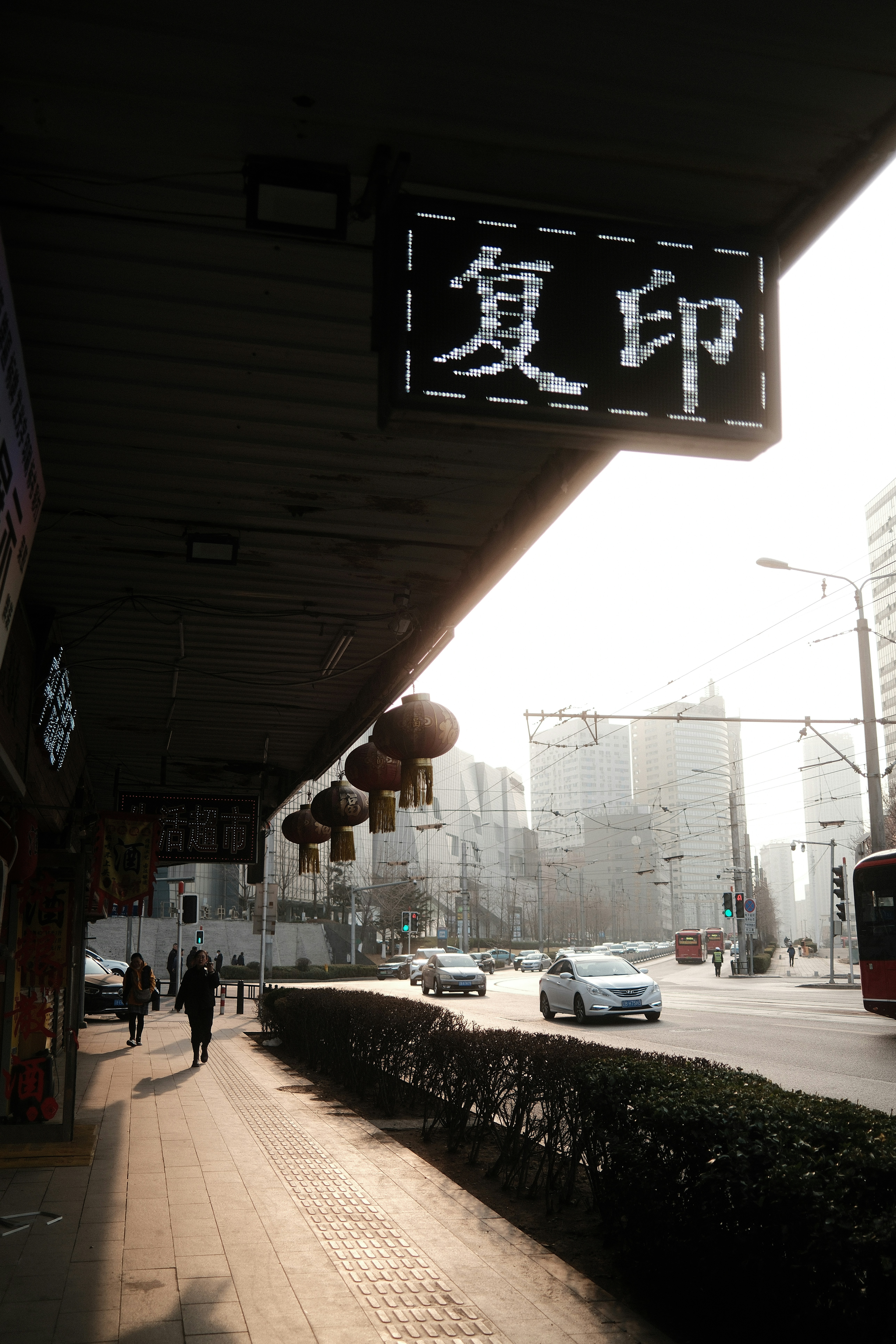 Lanterns and traffic fade into a city street under a neon-lit sign