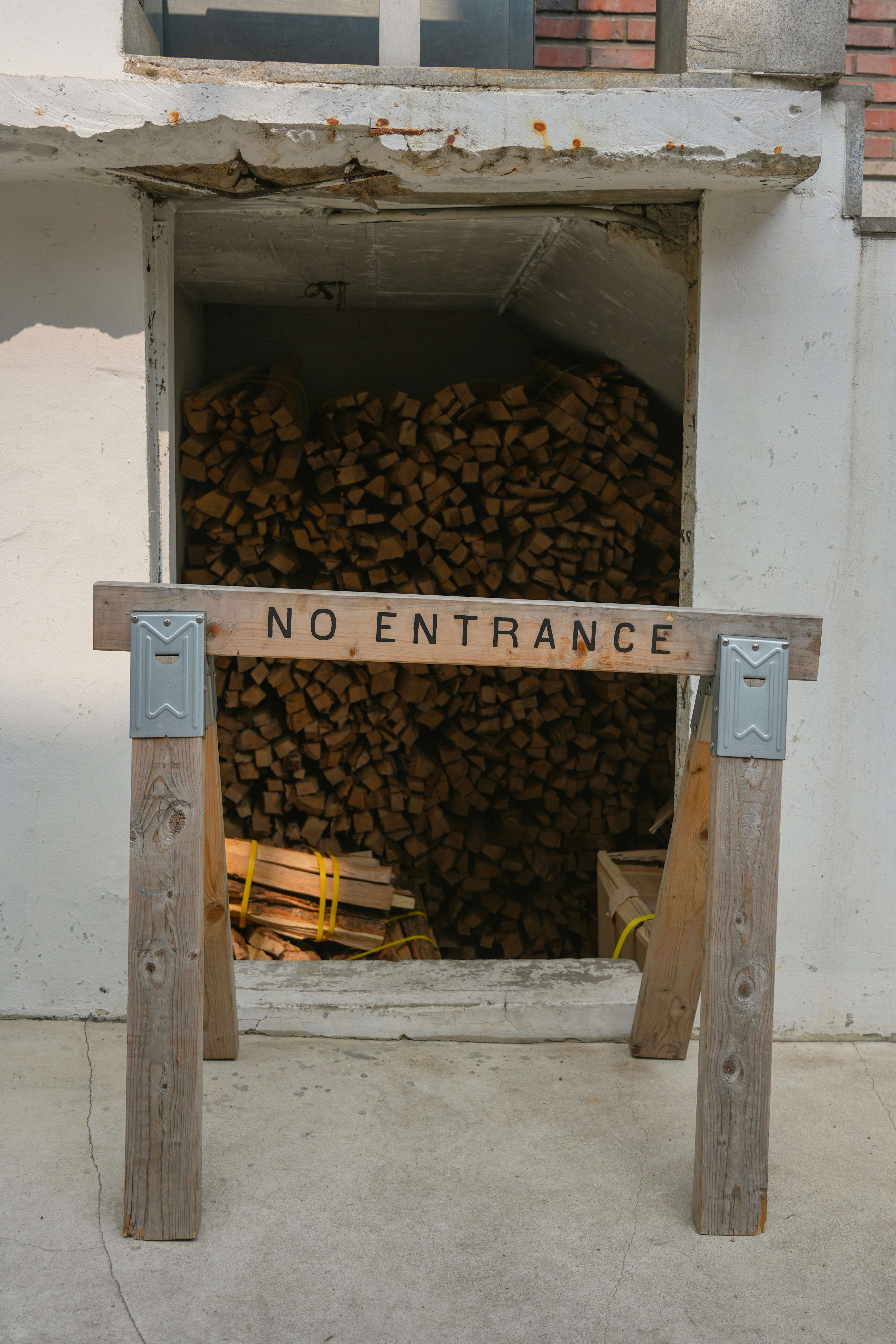 No Entrance: Stacked Firewood Behind a Weathered Barrier