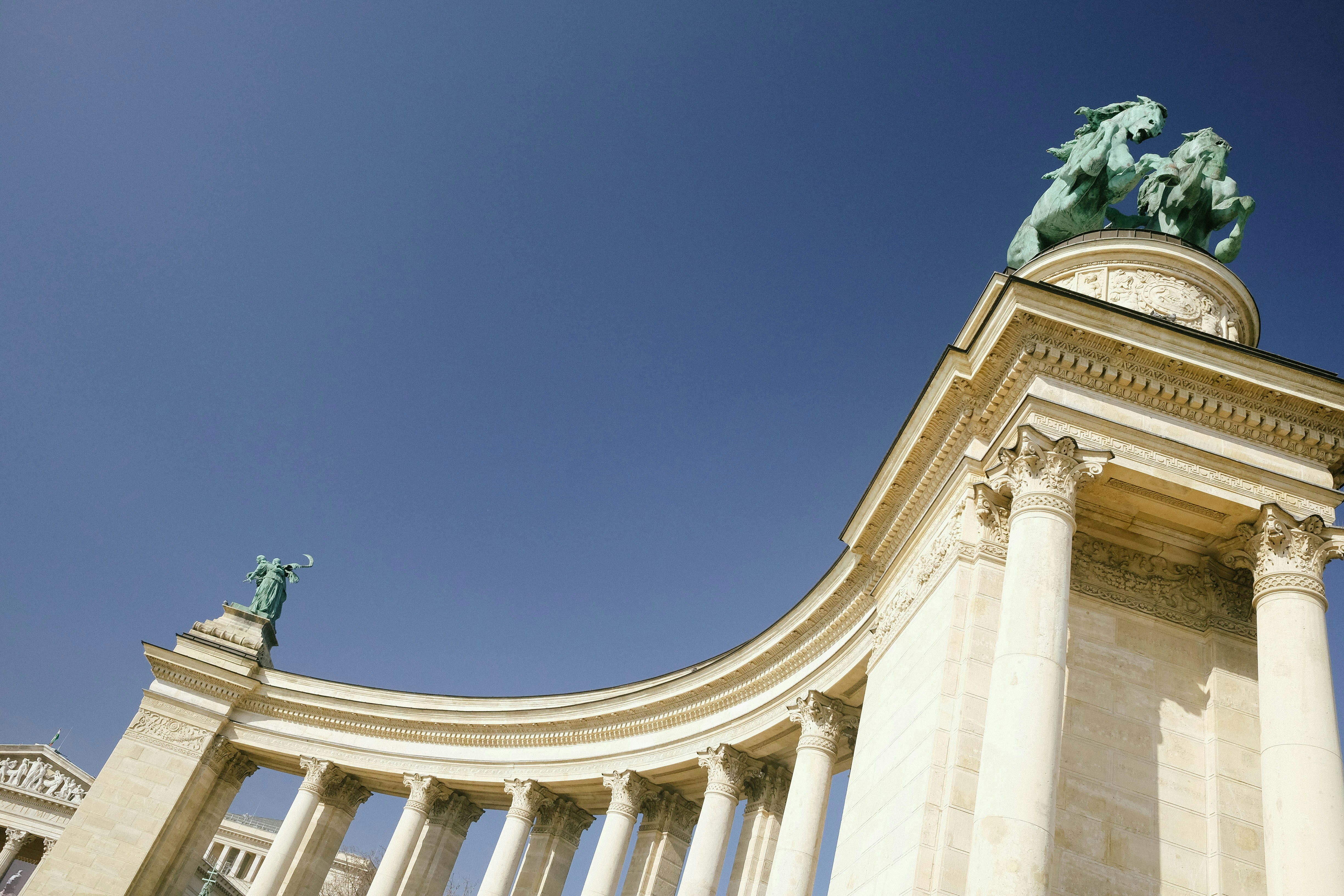 Statues Over an Arc: Sunlit Neoclassical Frieze Under a Clear Sky
