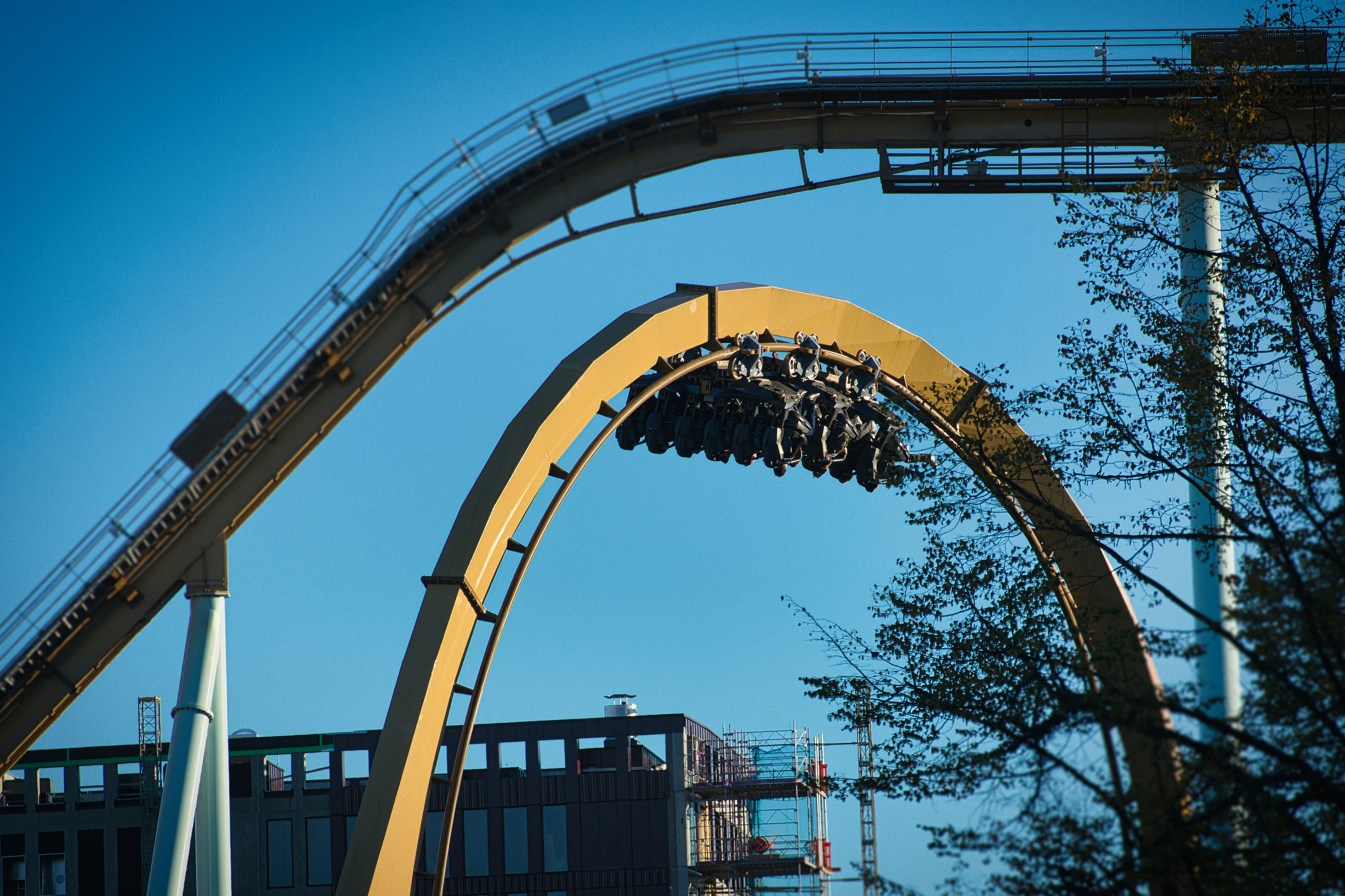 Arcing Threshold: A Golden Roller Coaster Crest Against A Clear Blue Sky