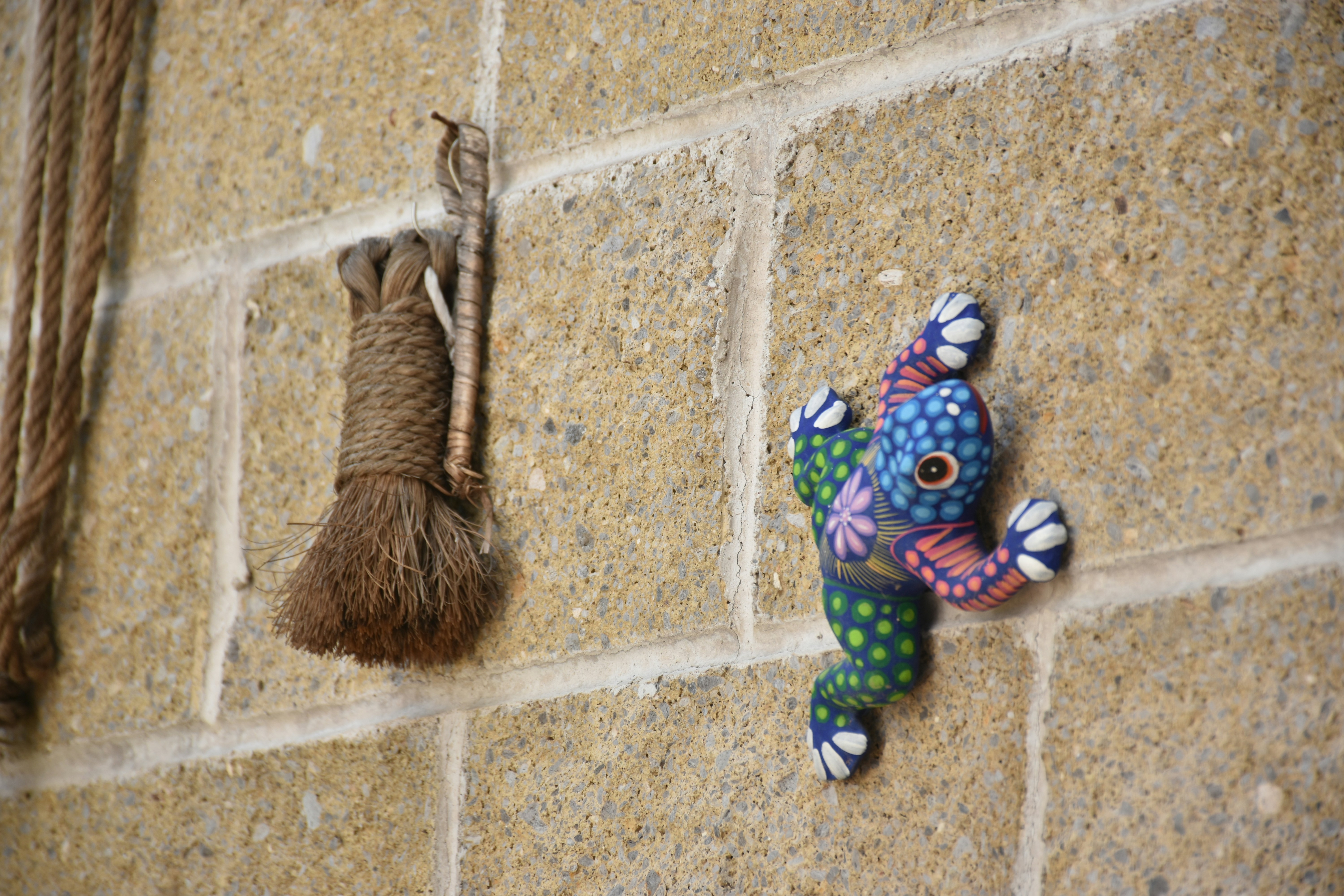 Colorful gecko charm stuck to a textured wall beside a rustic broom