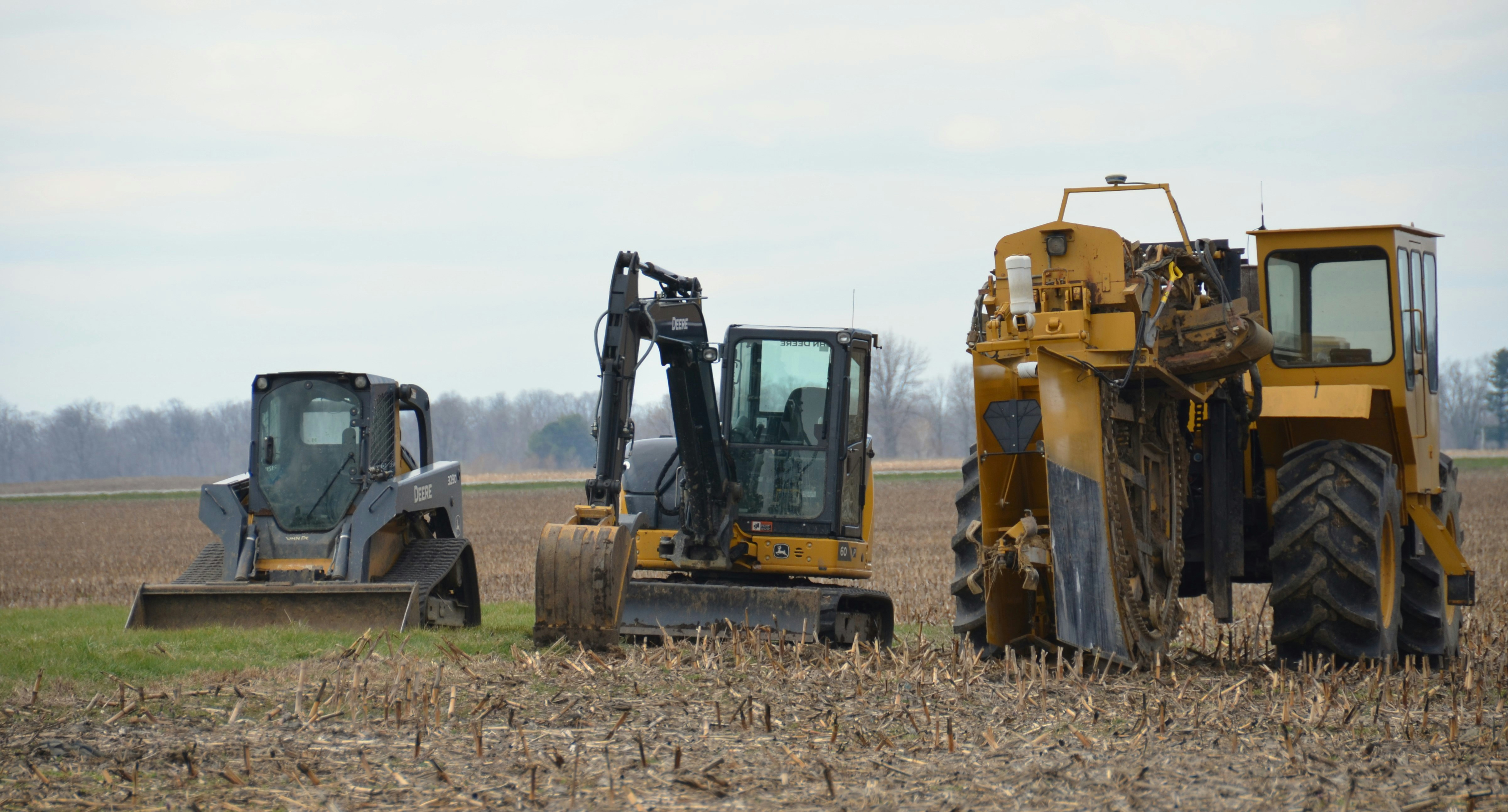 Three Heavy Machines Resting in a Harvested Field