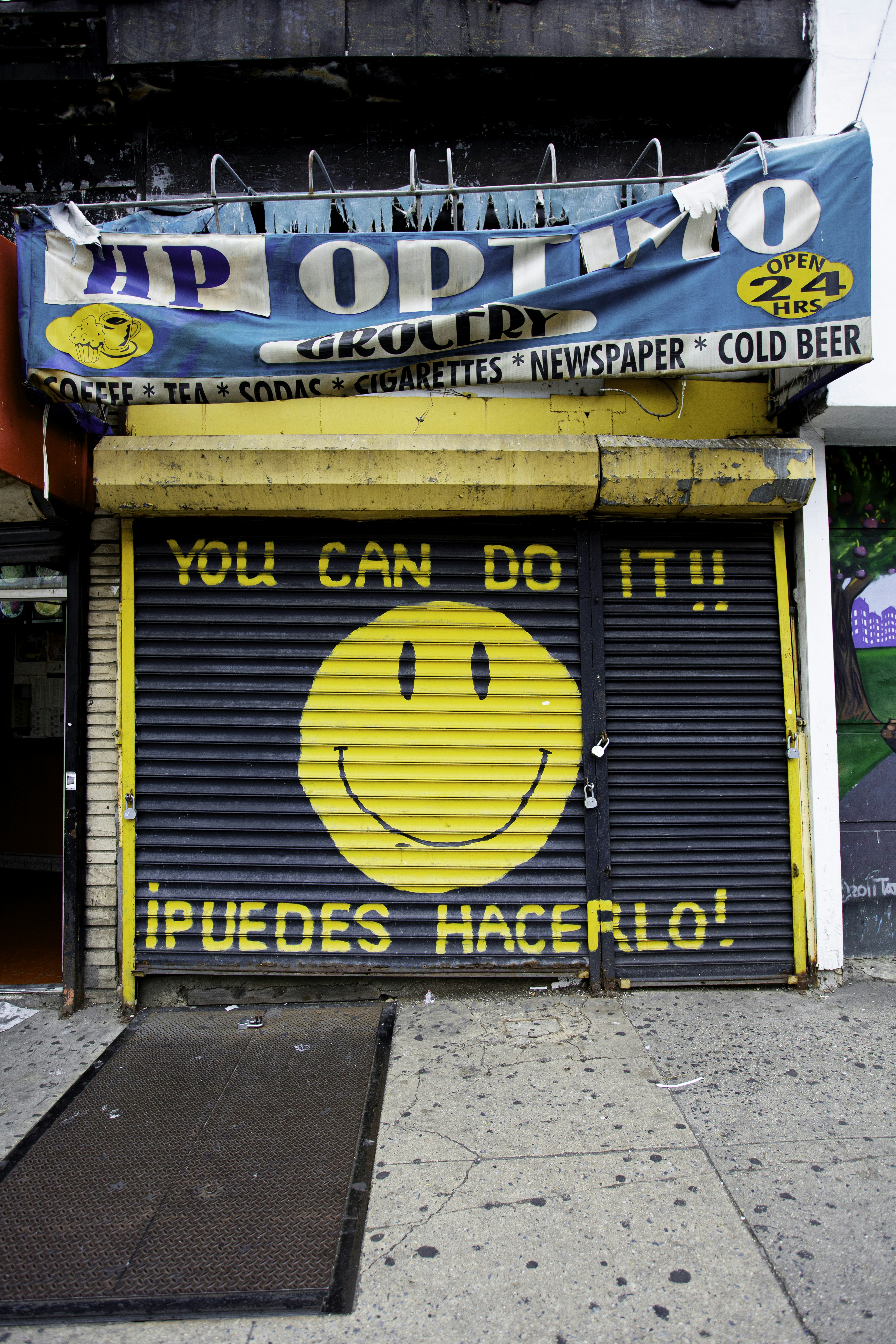 Yellow Smiley Gate: A Motivational Street GRAFFITI Banner Above a Shuttered Storefront