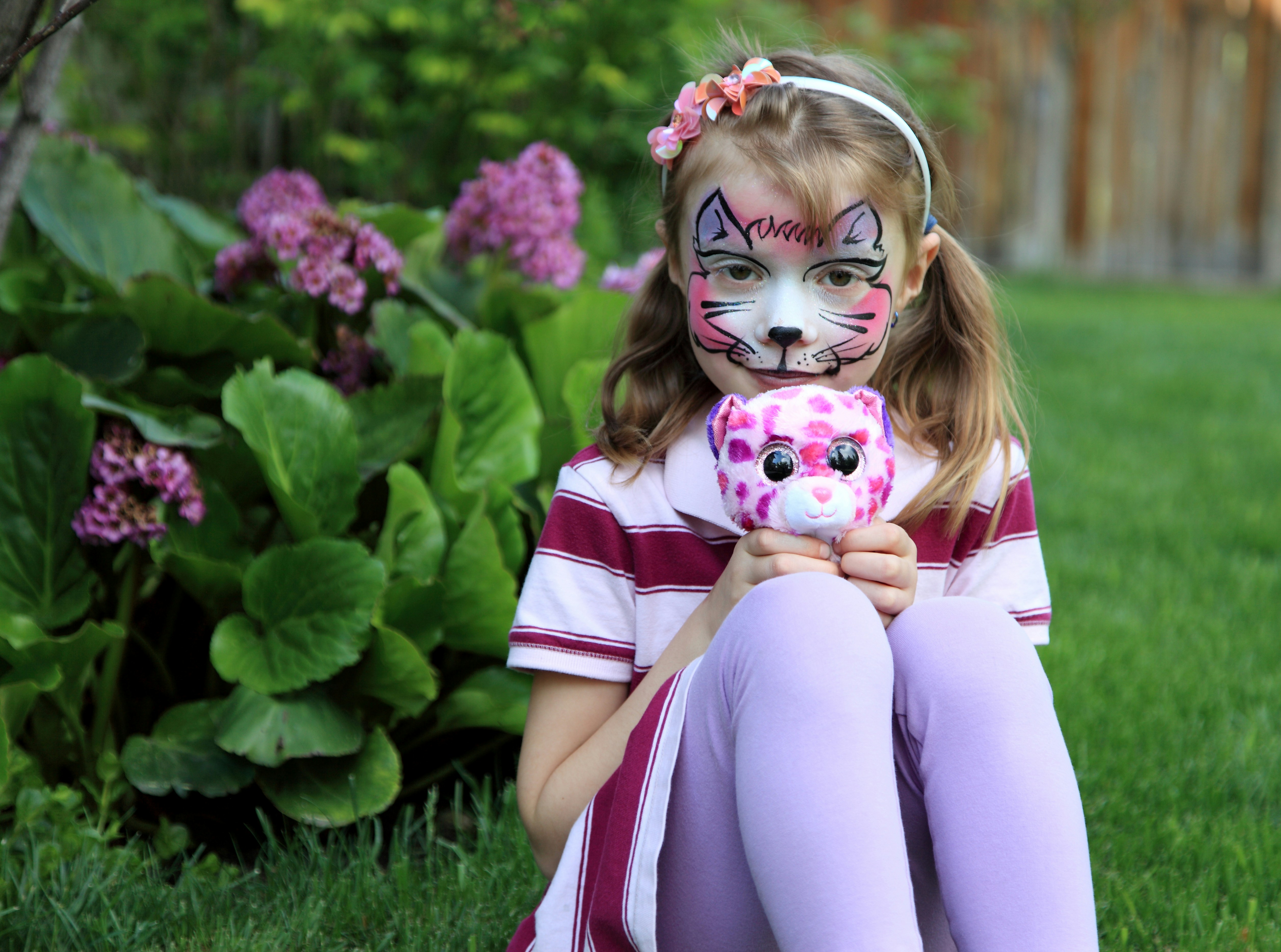 Painted whiskers and giggles: a girl with a tiger face holds a stuffed friend