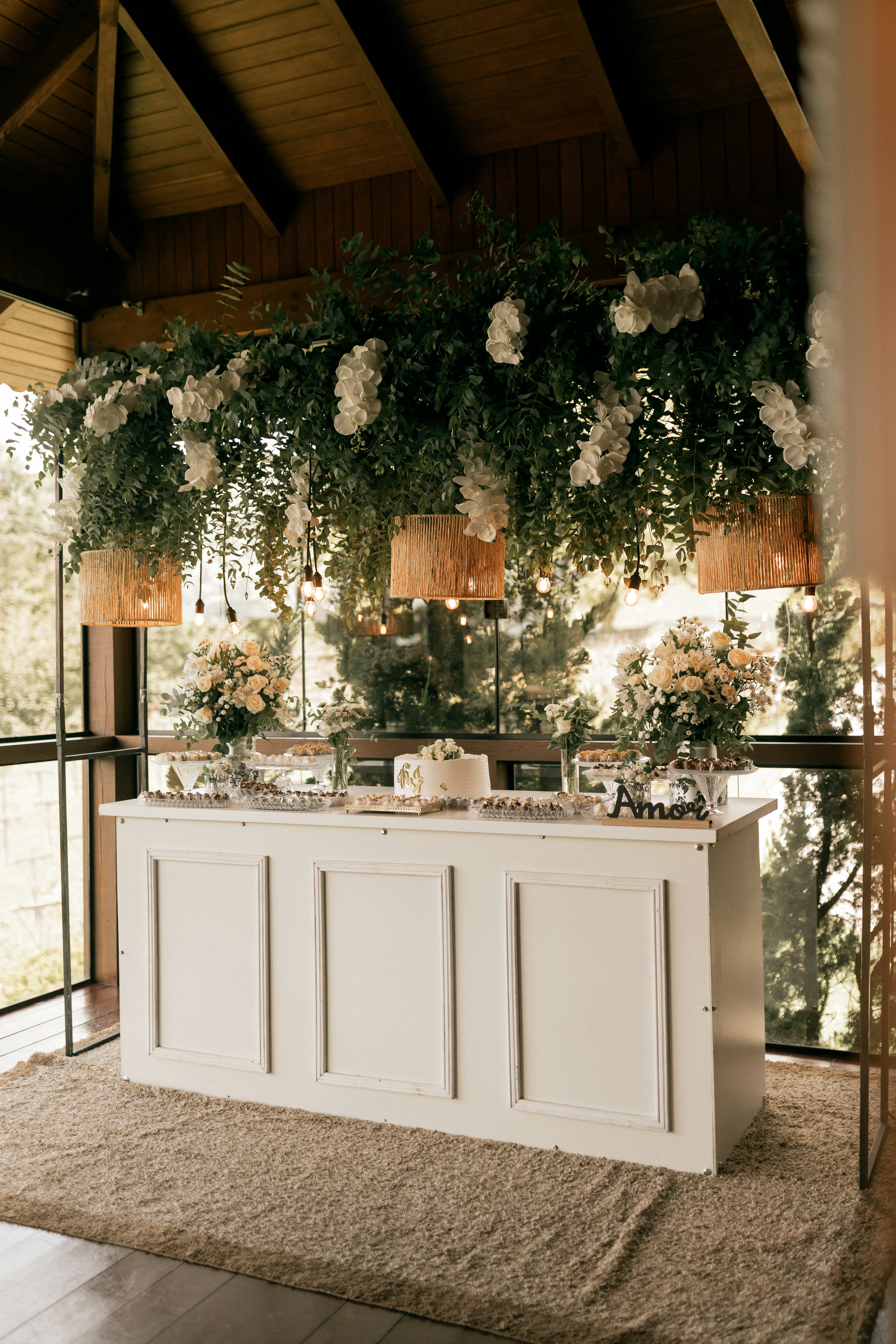 Floral canopy over a white dessert bar at a sunlit wedding venue