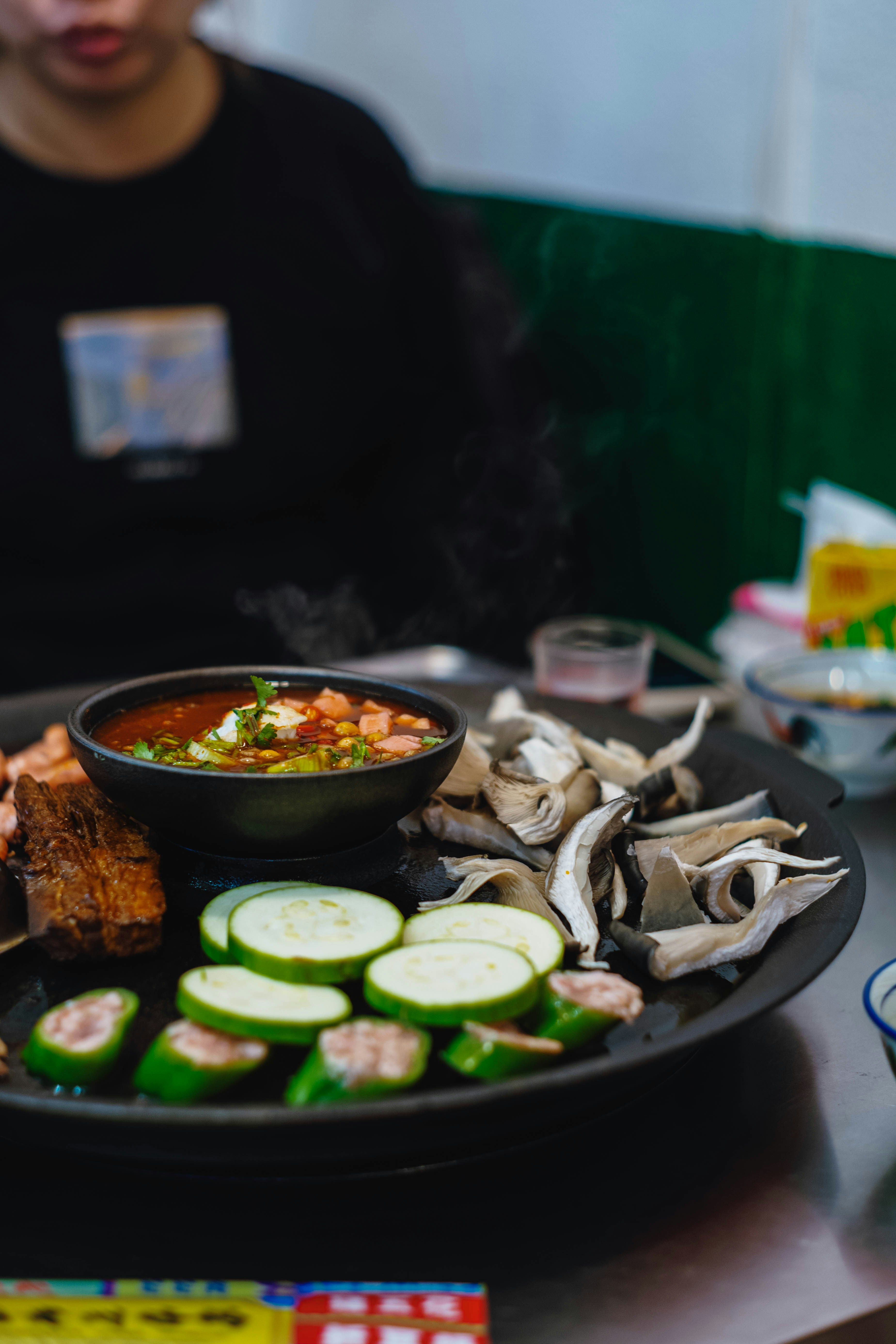 Plate of steaming Asian stew with grilled vegetables and mushrooms at a casual street table