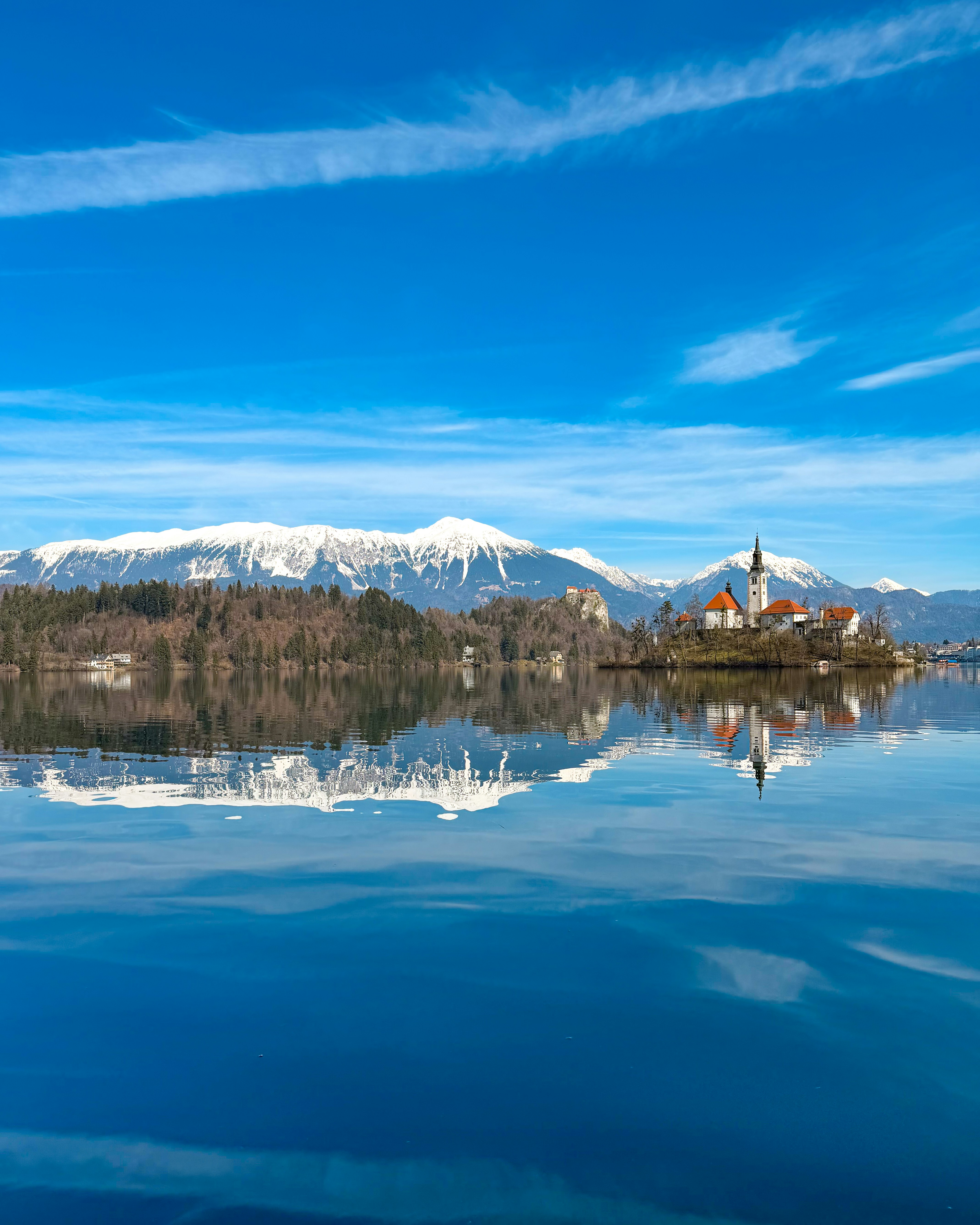 Snow-kissed Peaks reflected: A tranquil lakeside church duel-edged by pines