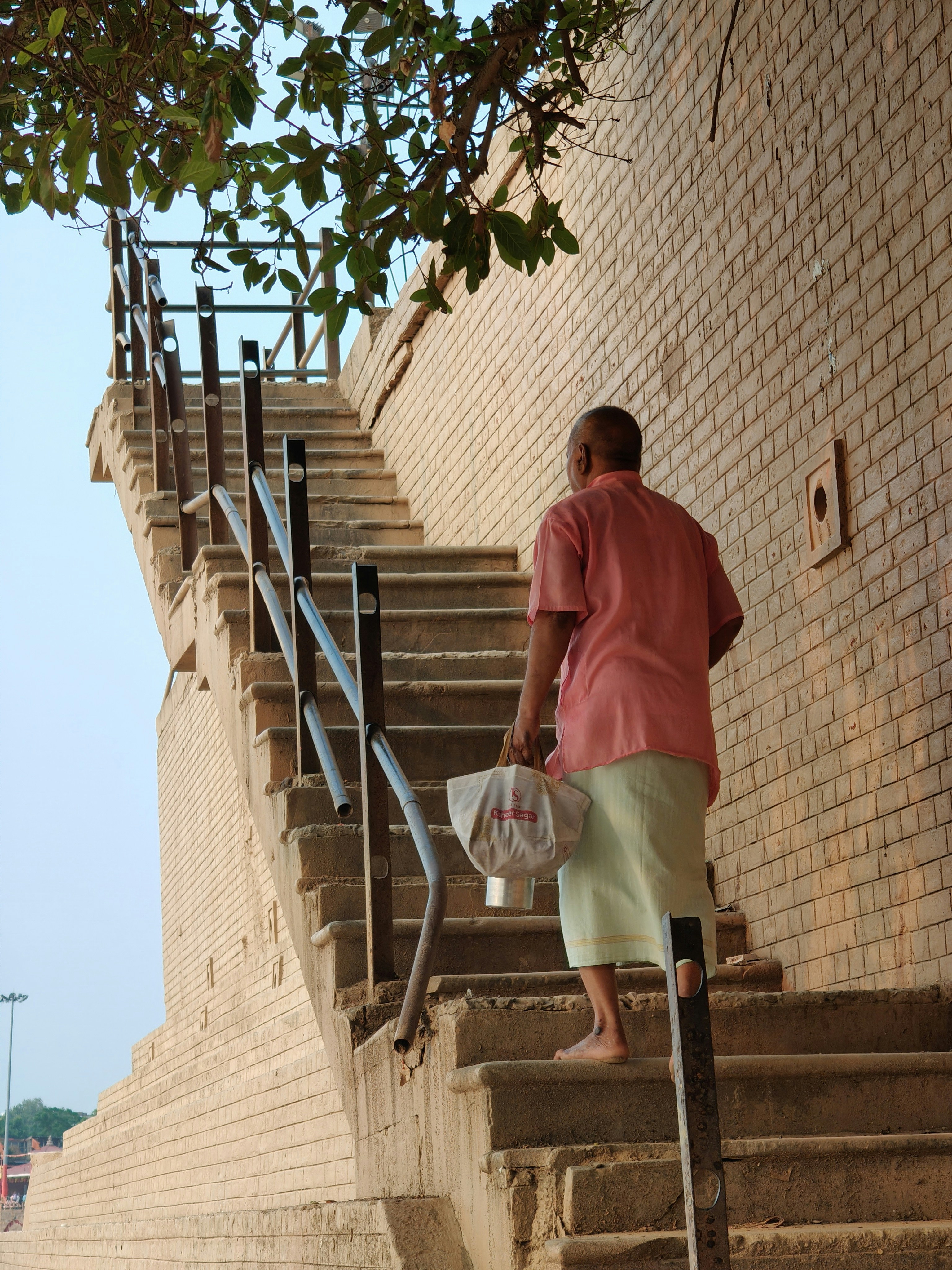 Rising Steps: Man in Coral Shirt Ascends a Sunlit Limestone Staircase