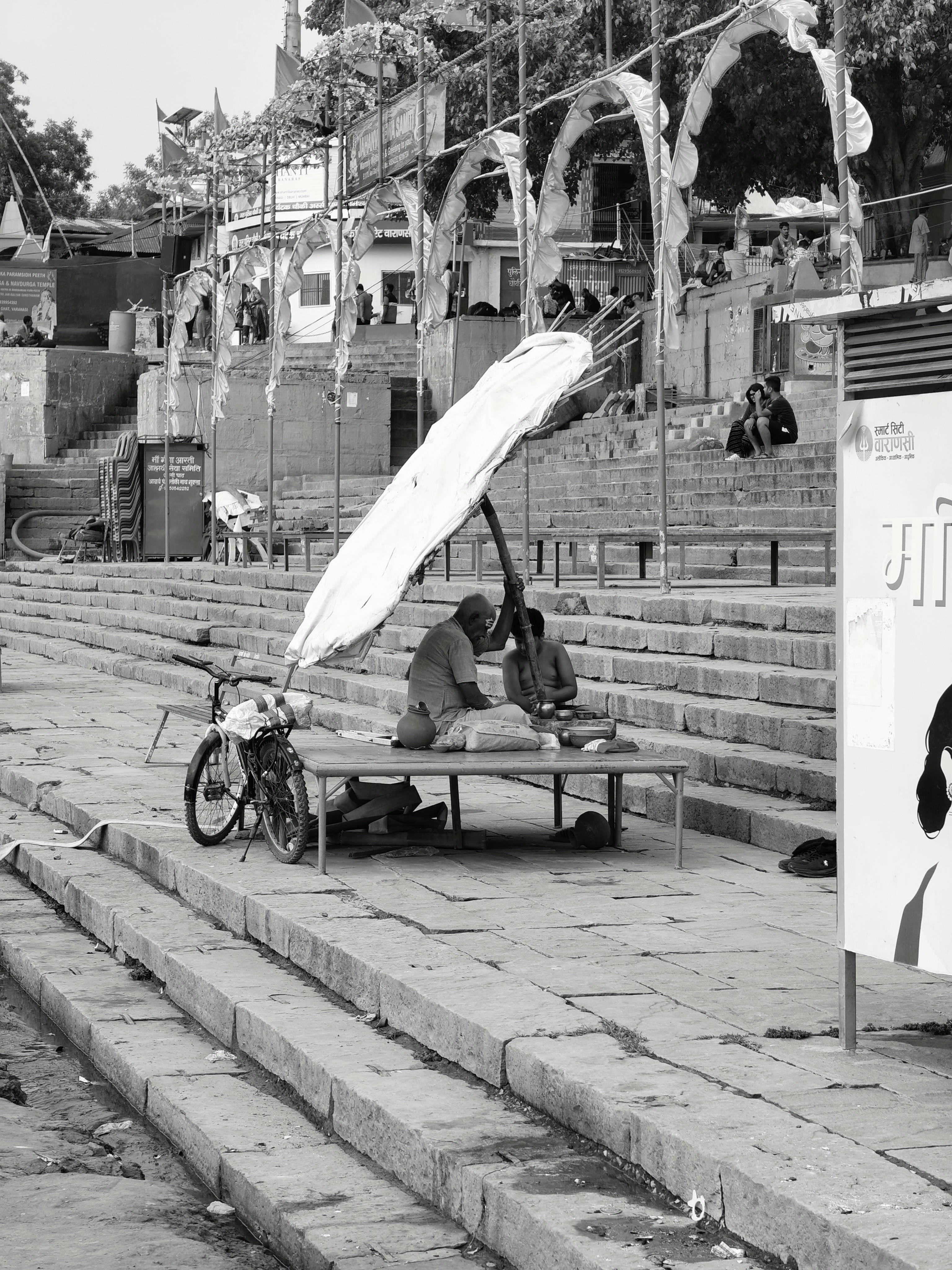 Street-side Shade: Vendor at Work Under a Shelter of Flags