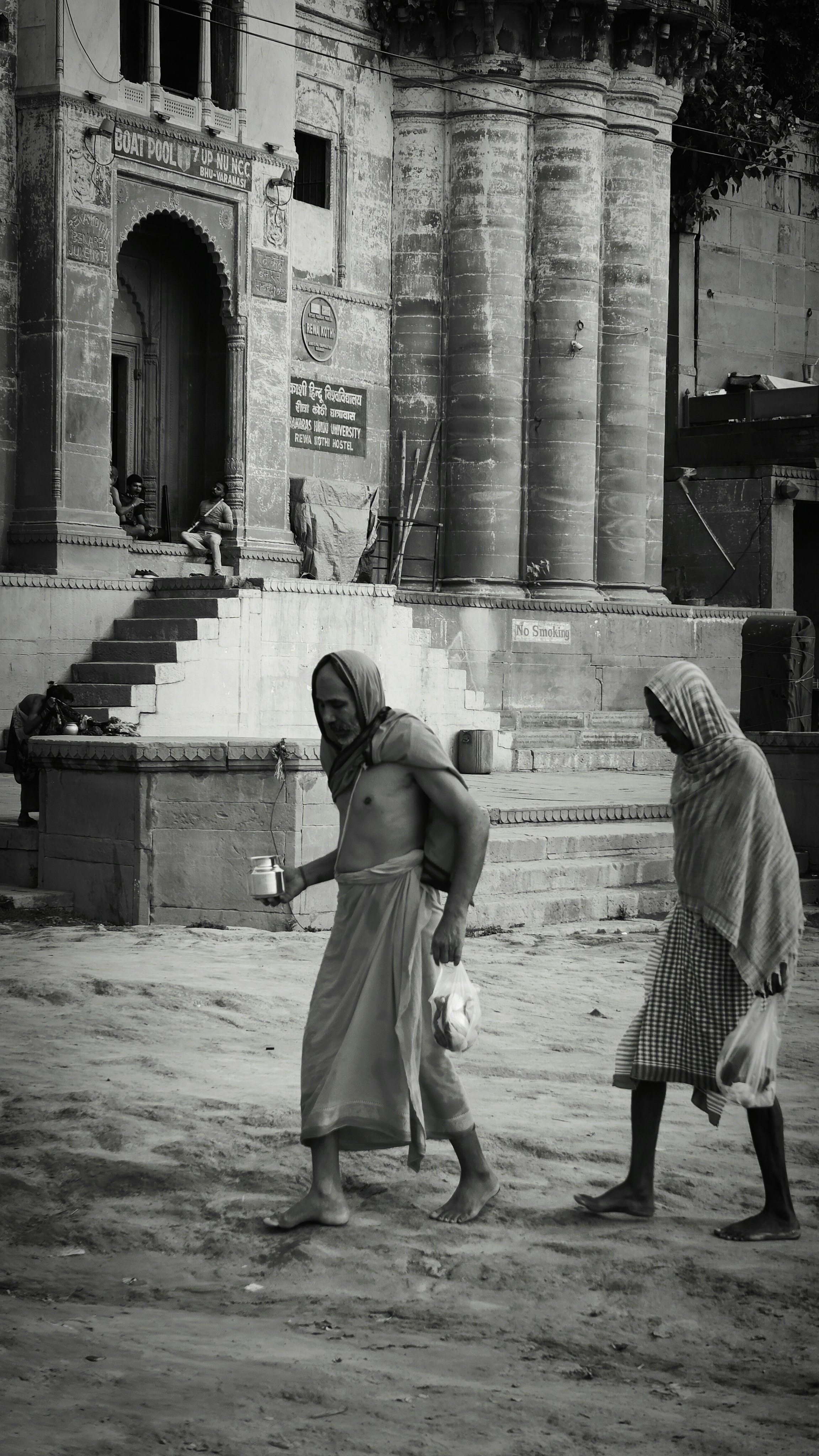 Two pilgrims in raised temple forecourt, shadowed by ancient pillars