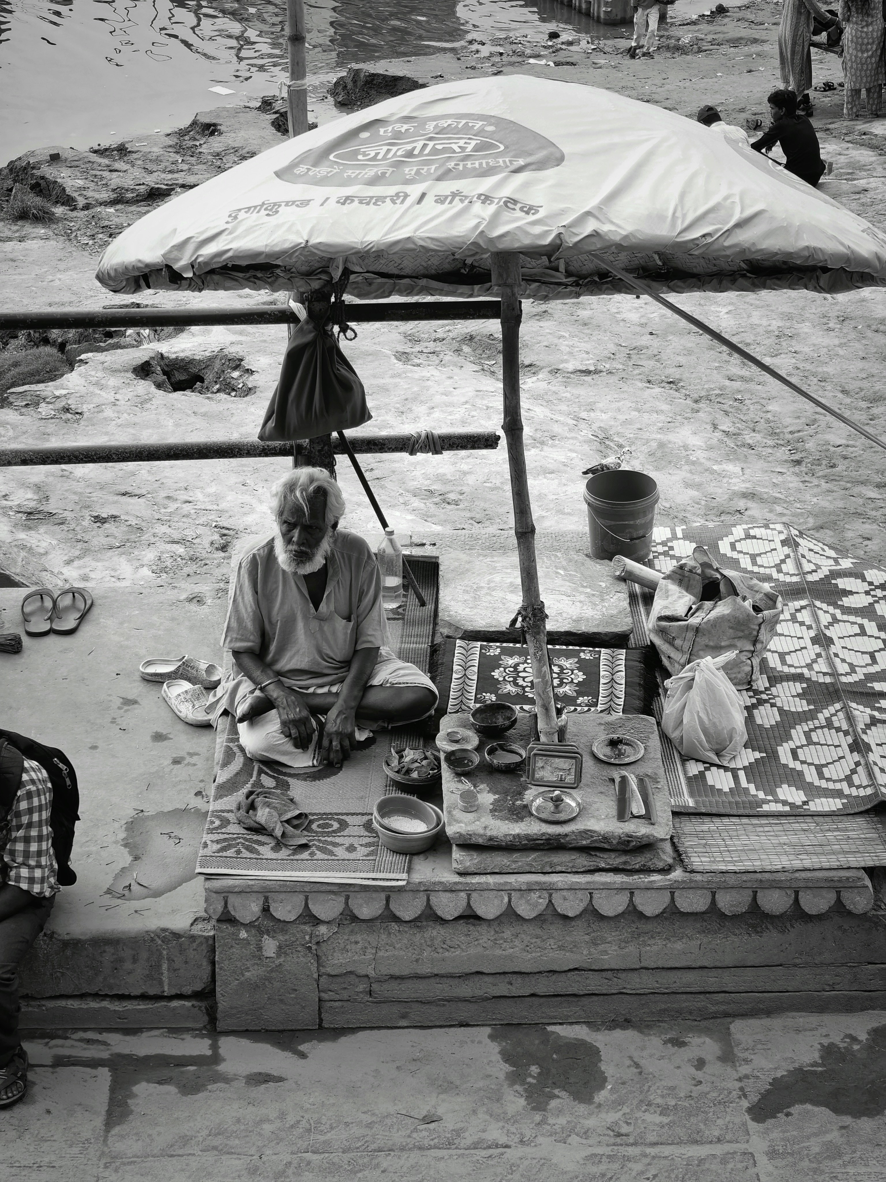 Old Vendor under a canopy: a quiet street ritual by the riverbank