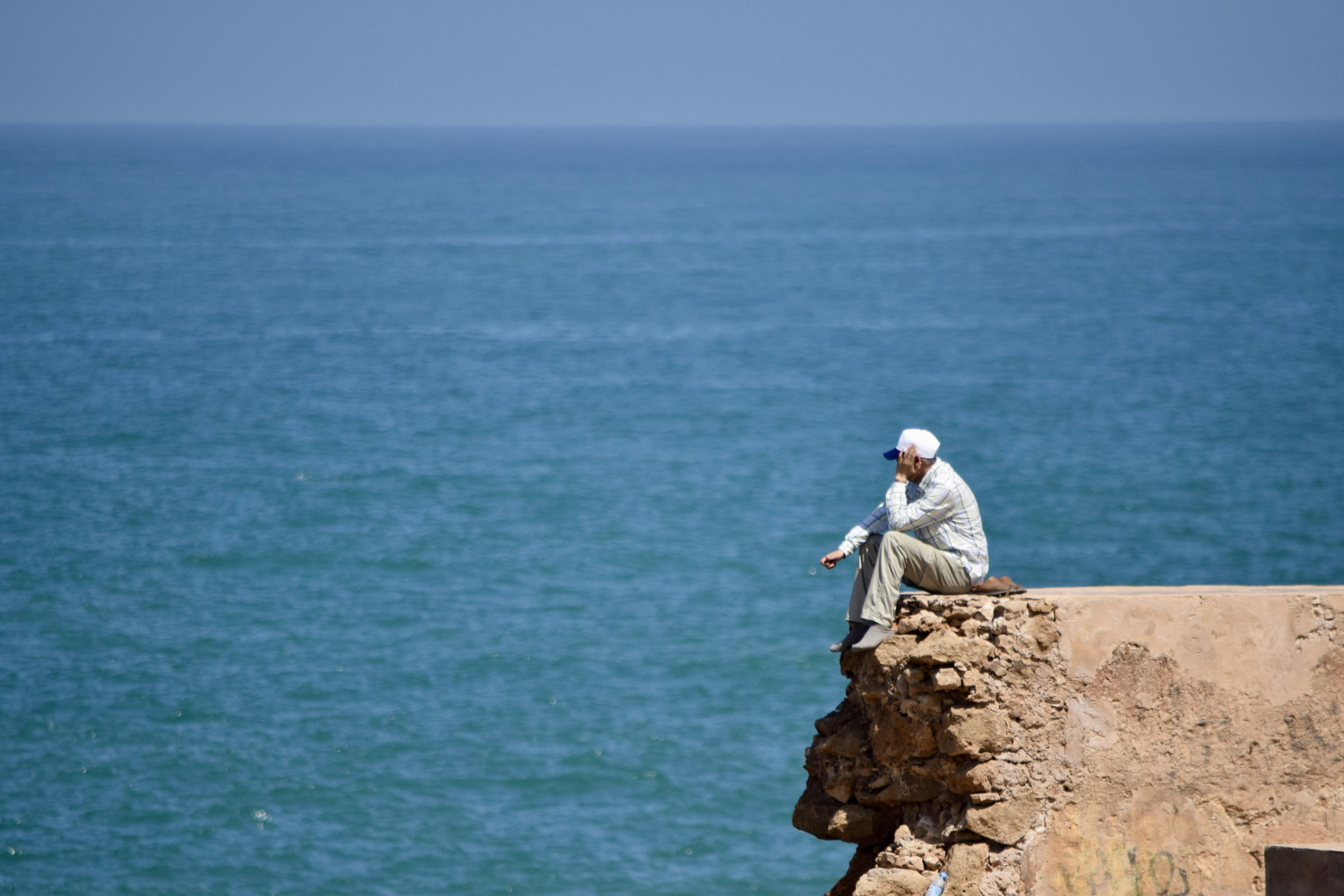 Seated silhouette at the cliff's edge over a calm sea