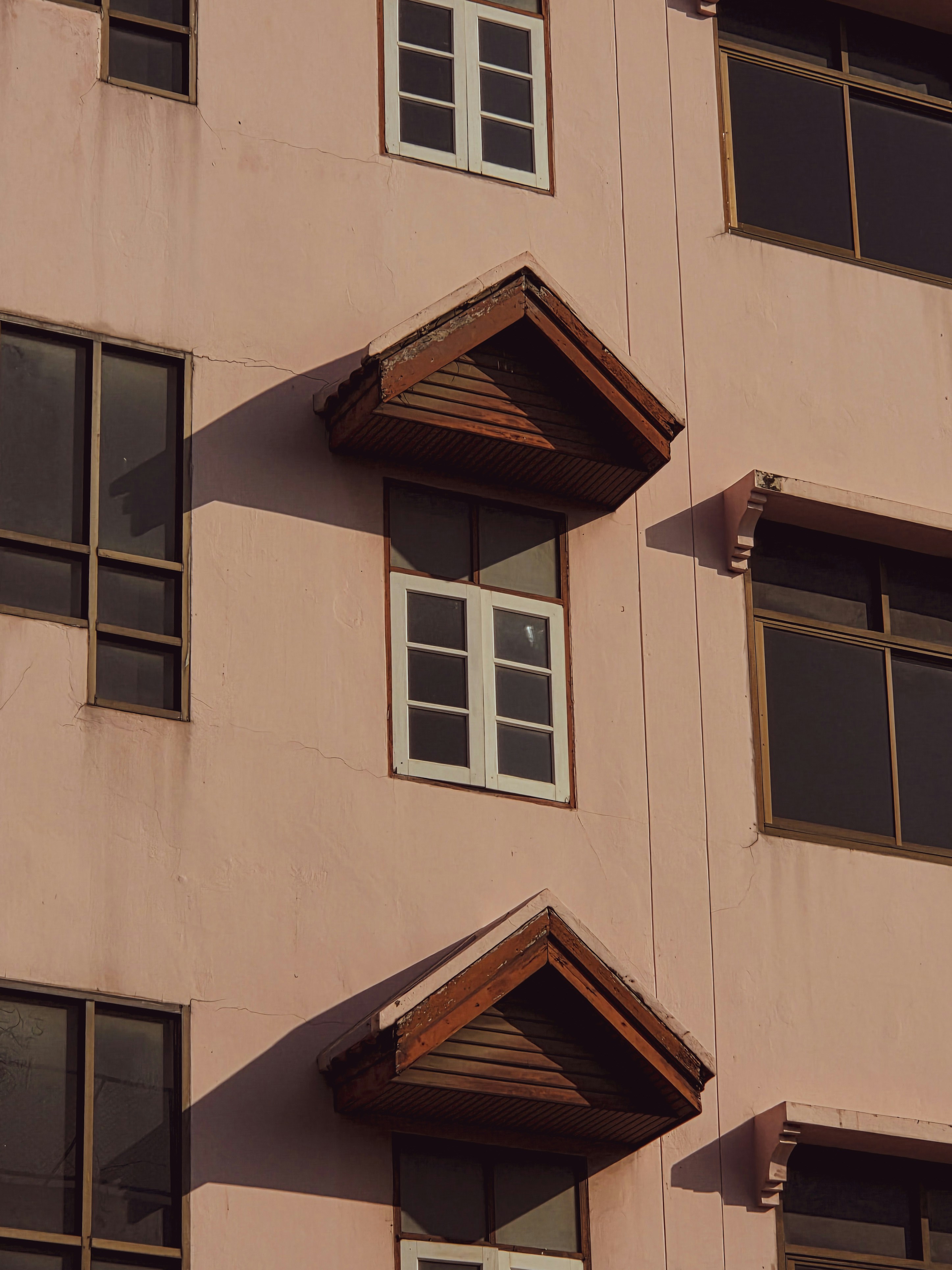 Sidelight casts warm shadows across a pale pink residential building with a repeating window pattern and wooden awnings.