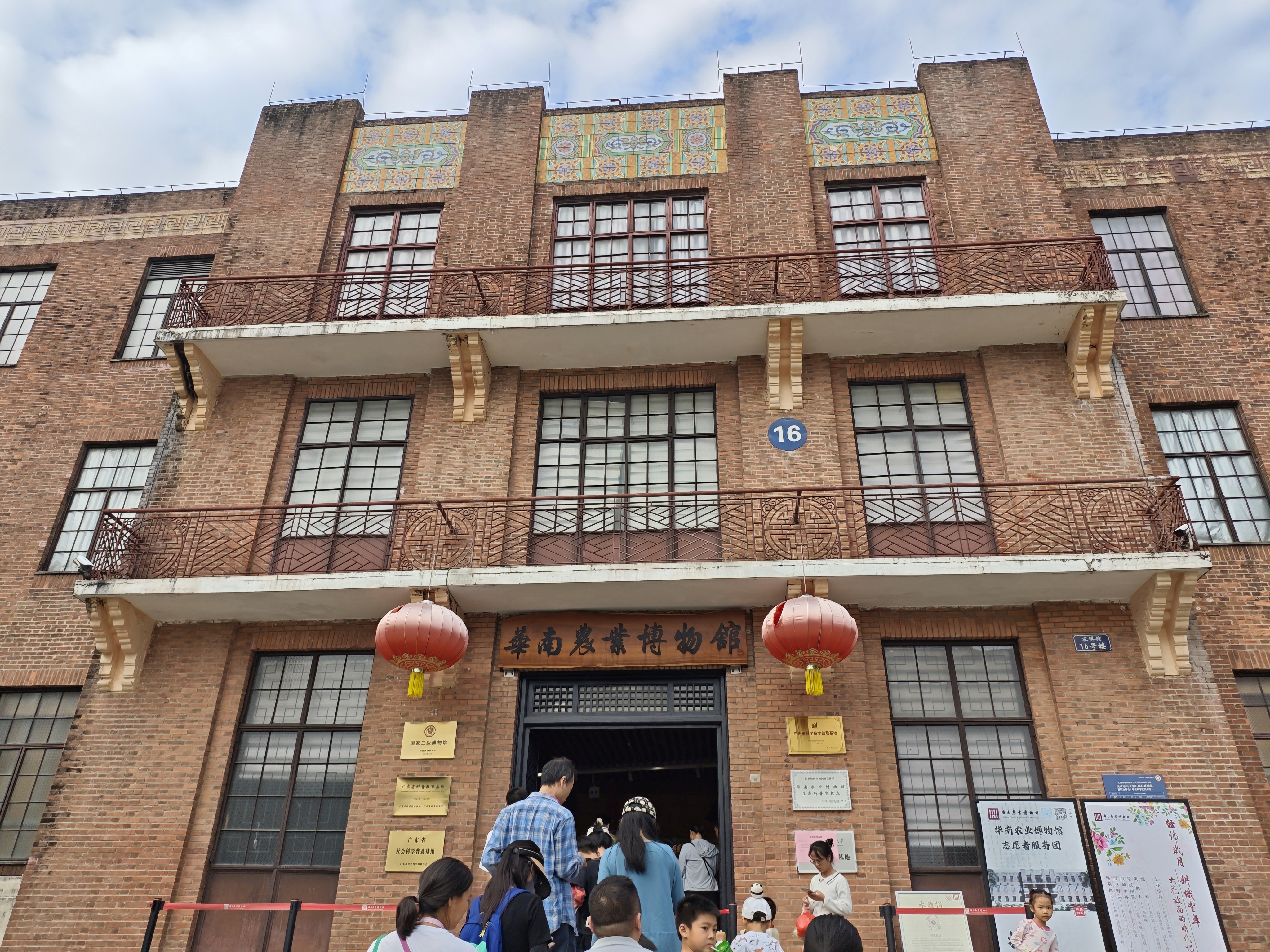 People enter a brick building with Chinese lanterns and signboards, suggesting a cultural or educational site.