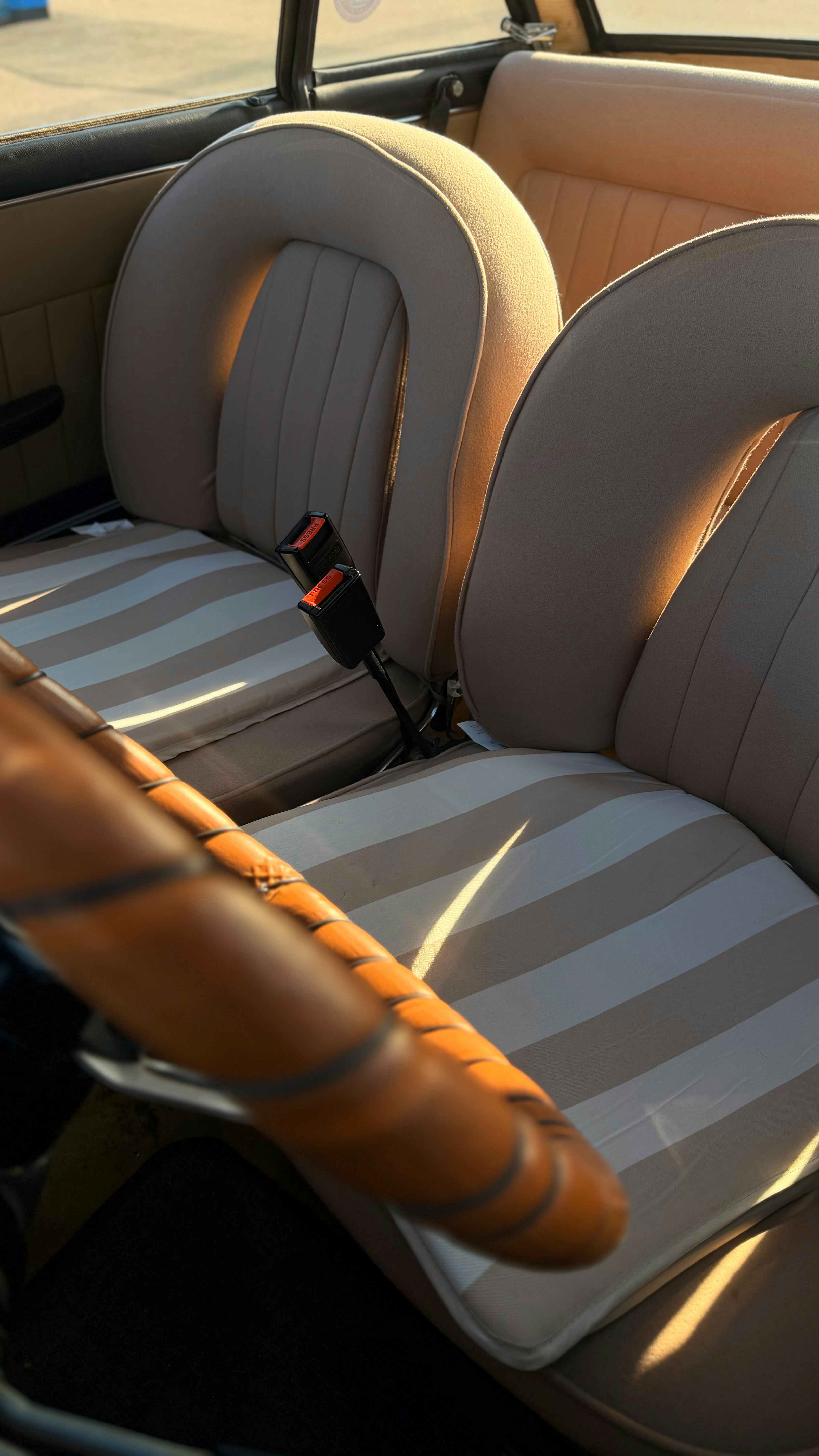 Sunlit Vintage Car Cabin: Striped Seats and Worn Leather Steering Wheel