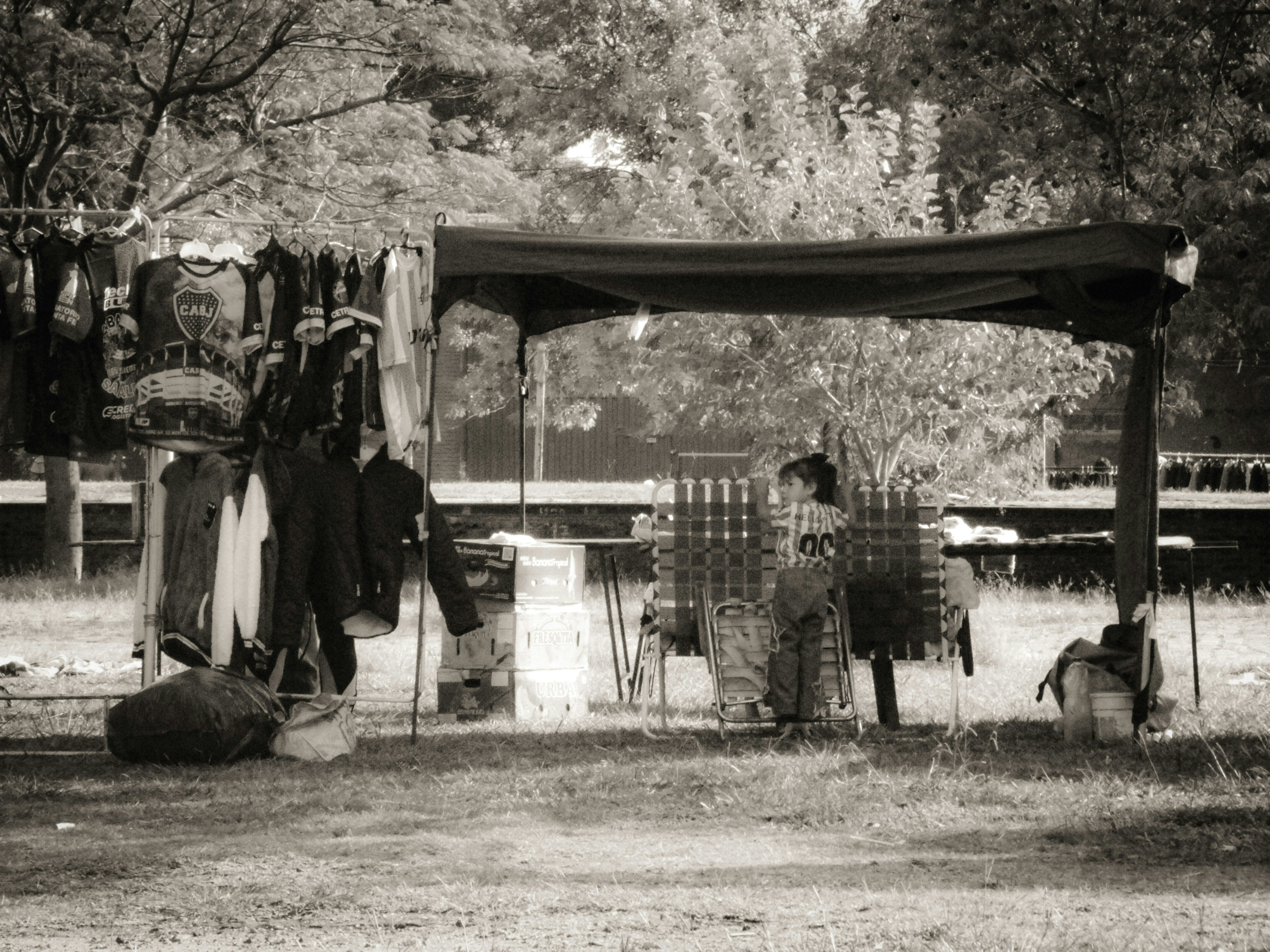 Vendors under a canopy with clothing and gear on display at a campsite market.
