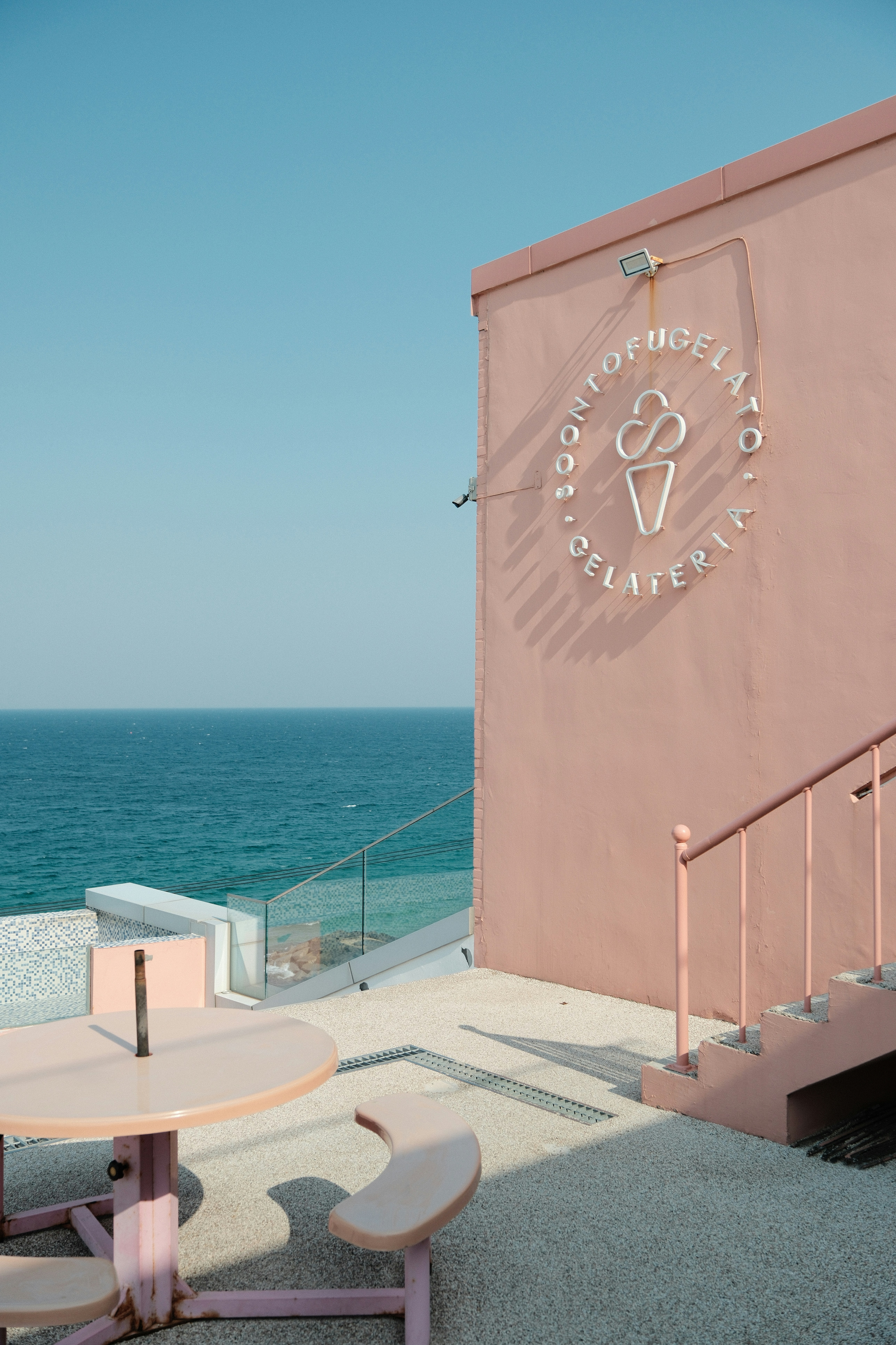 Pastel terrace by the sea: pink walls, soft shadows, and ocean breeze