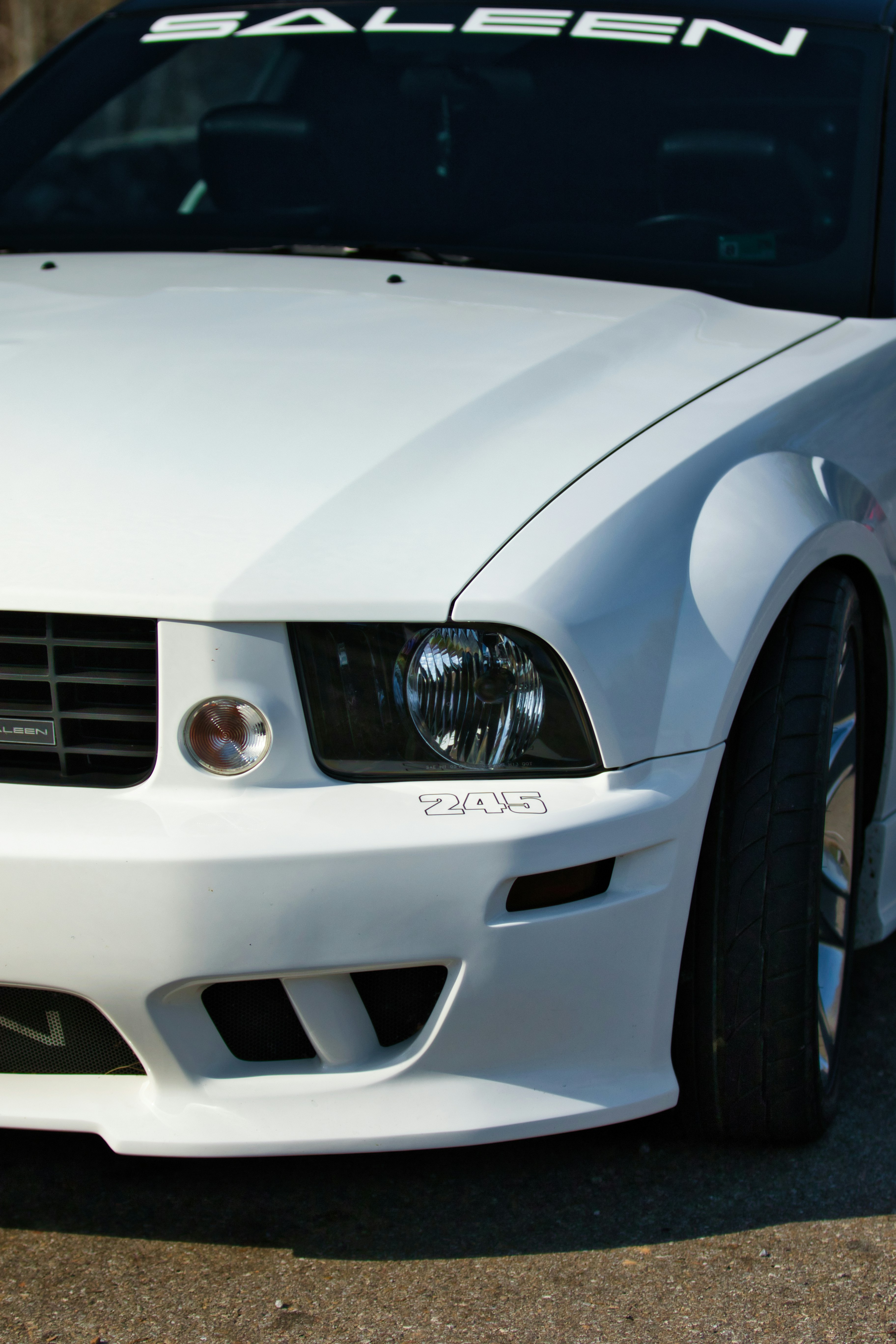 White Nissan-2K on glossy pavement: a close-up of the front-right fender and wheel