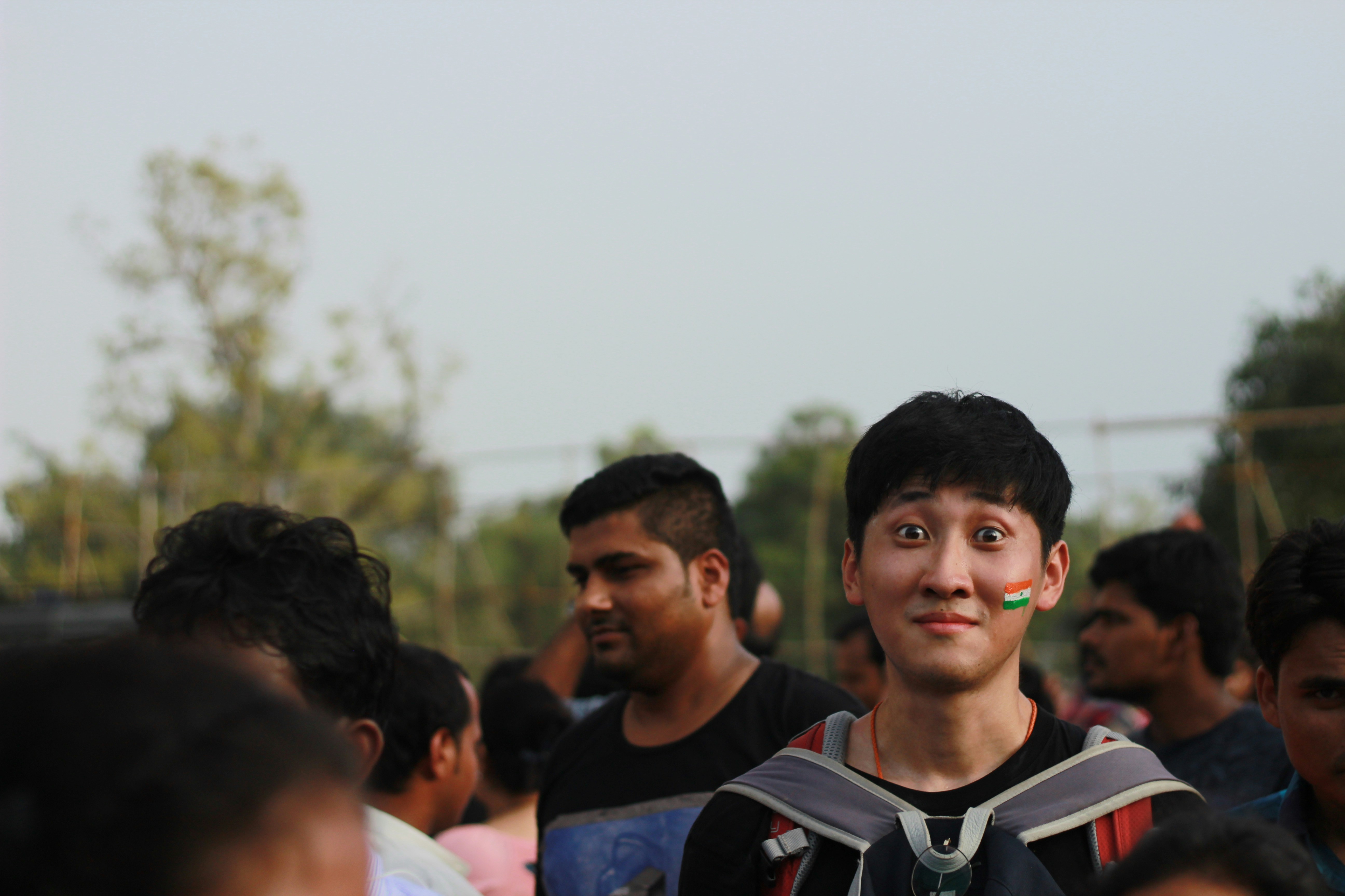 Cheerful Crowded Moment: A young man with face paint stands out among festival attendees