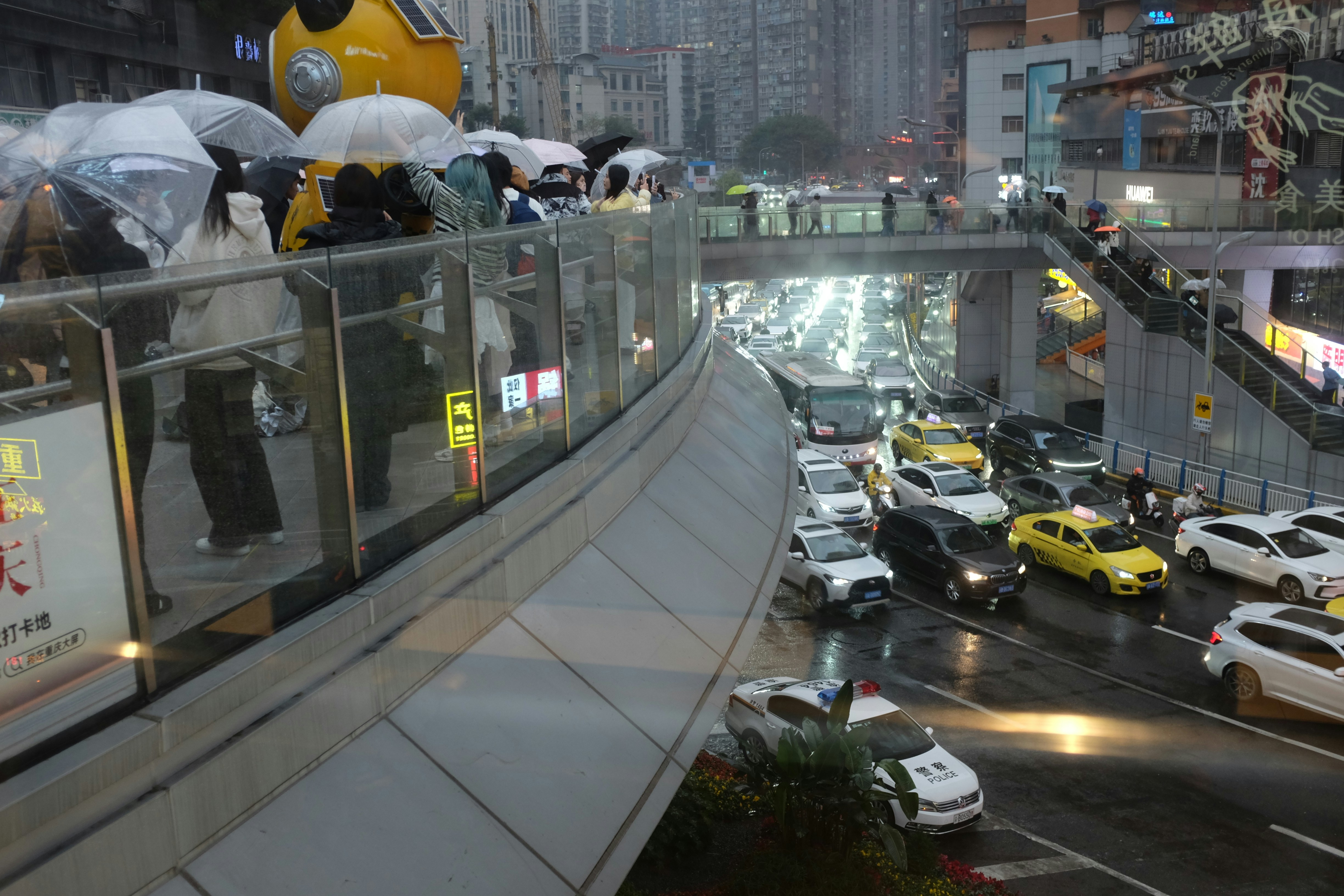 People on an elevated walkway overlook a rain-soaked urban crossroad at dusk