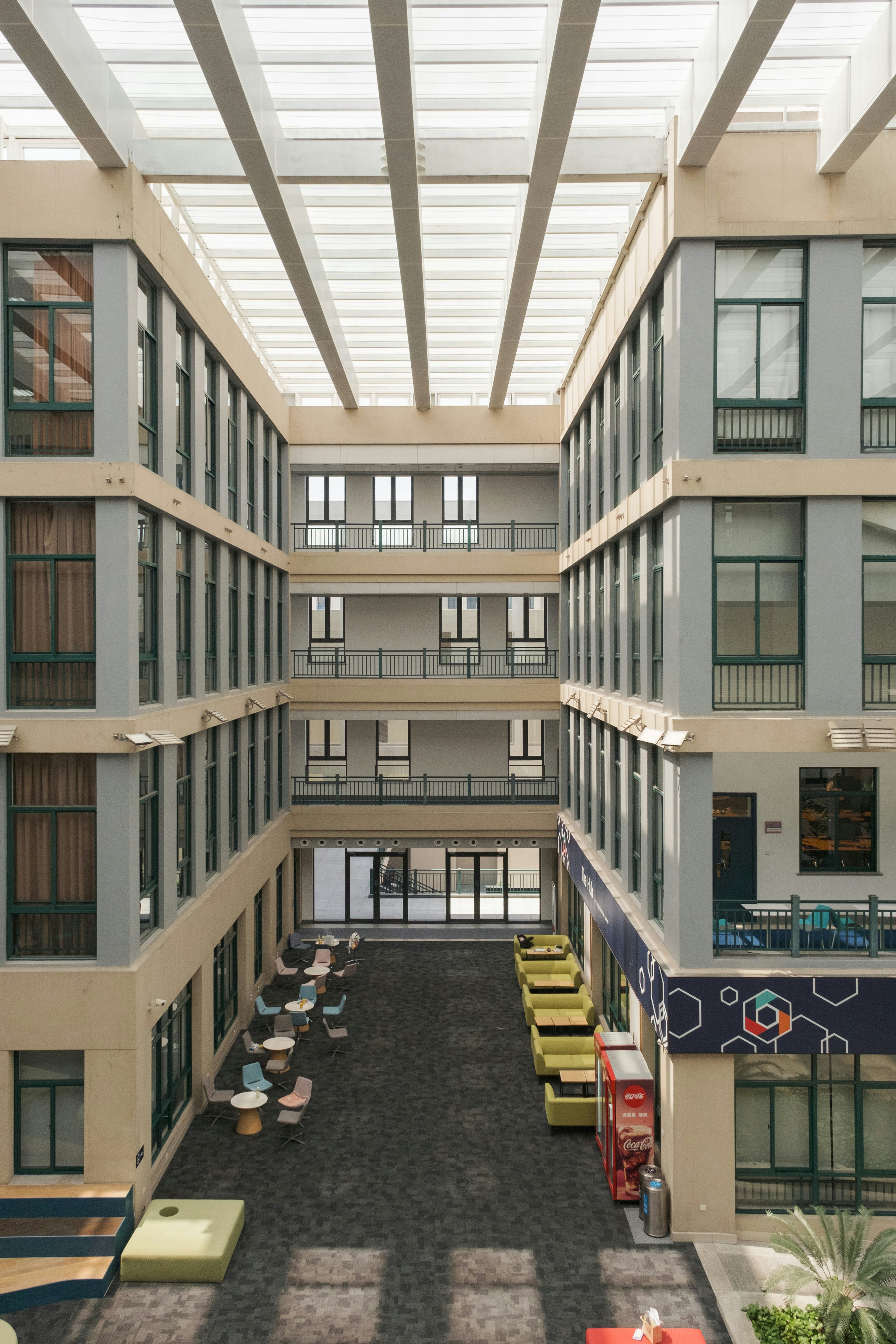 Interior courtyard of a modern building with symmetrical wings, sunlit glass windows, and a cozy lounge area along the lower level.