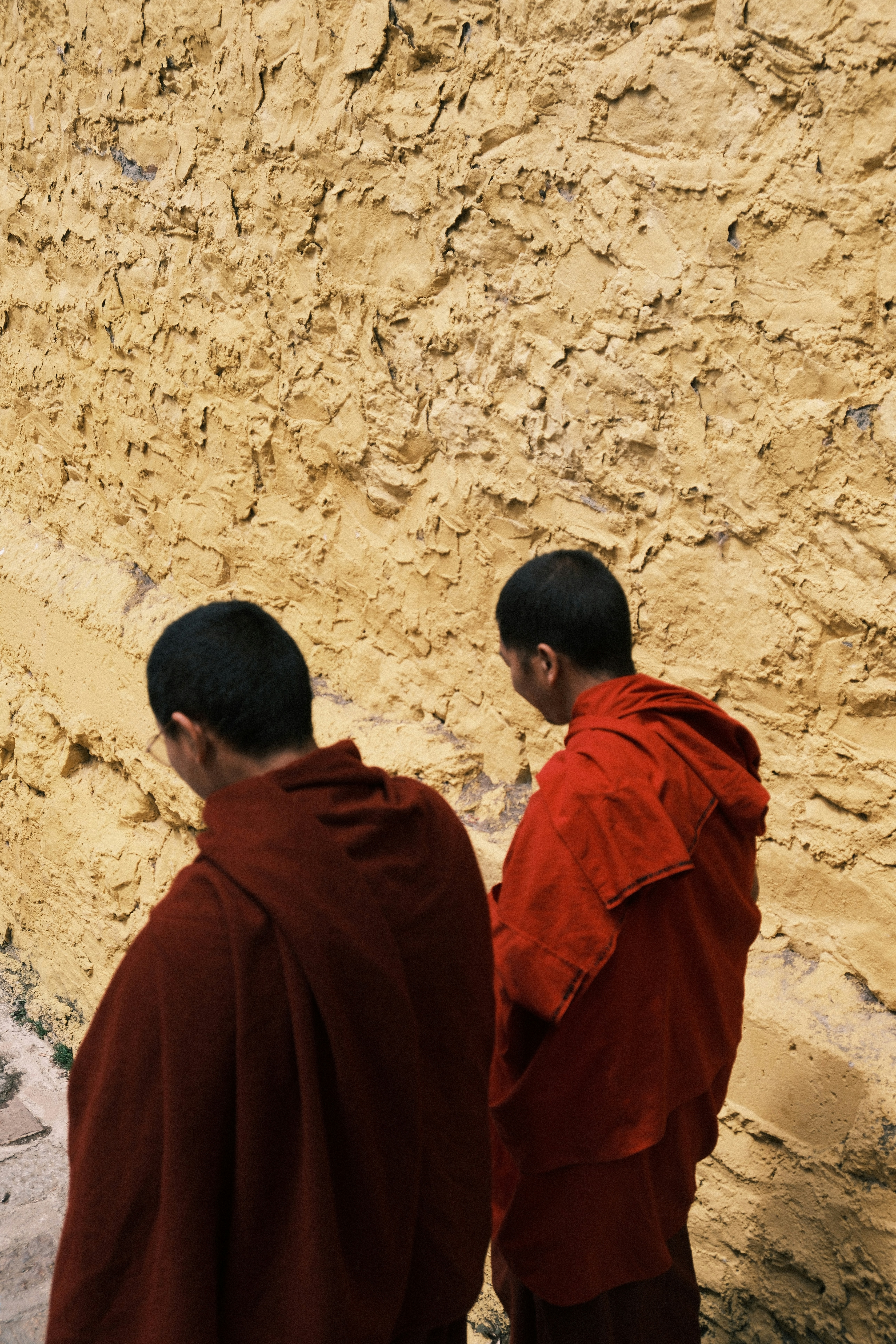 Two Monks in Rust-Colored Robes by a Sunlit Wall
