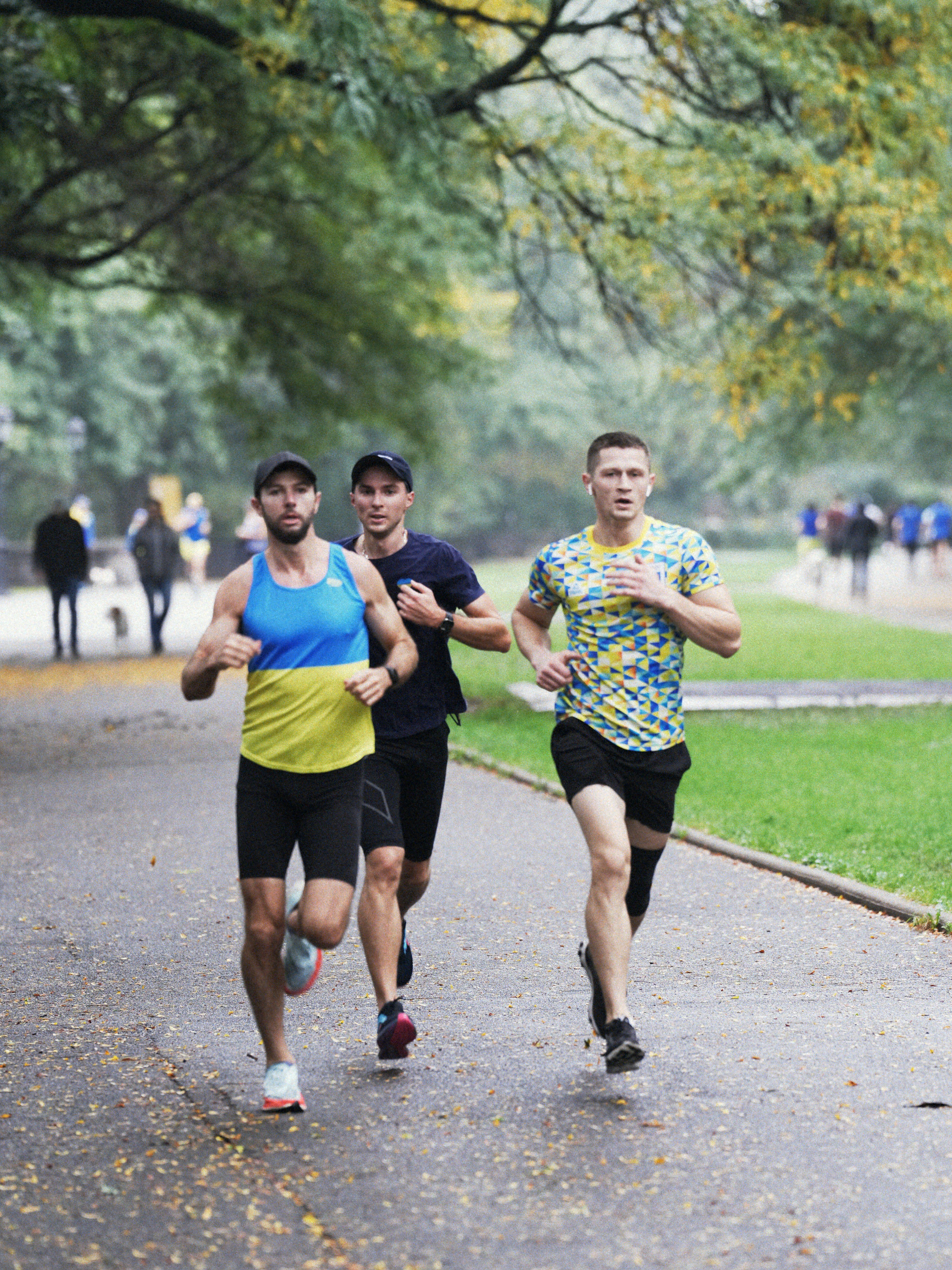 Three runners surge along a park path under a canopy of autumn leaves