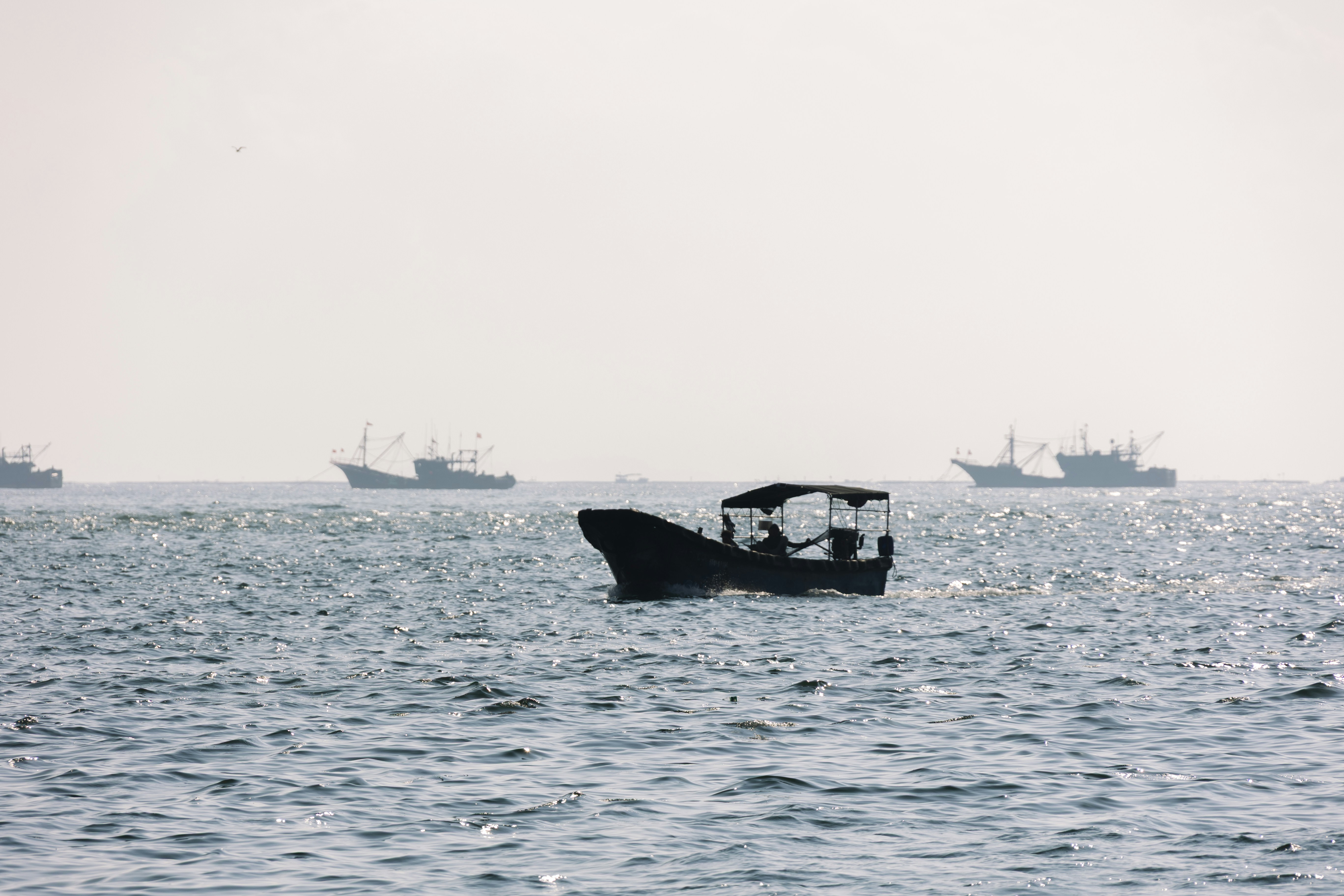 Silhouette of a Small Boat Amid Distant Harbor Traffic at Dusk