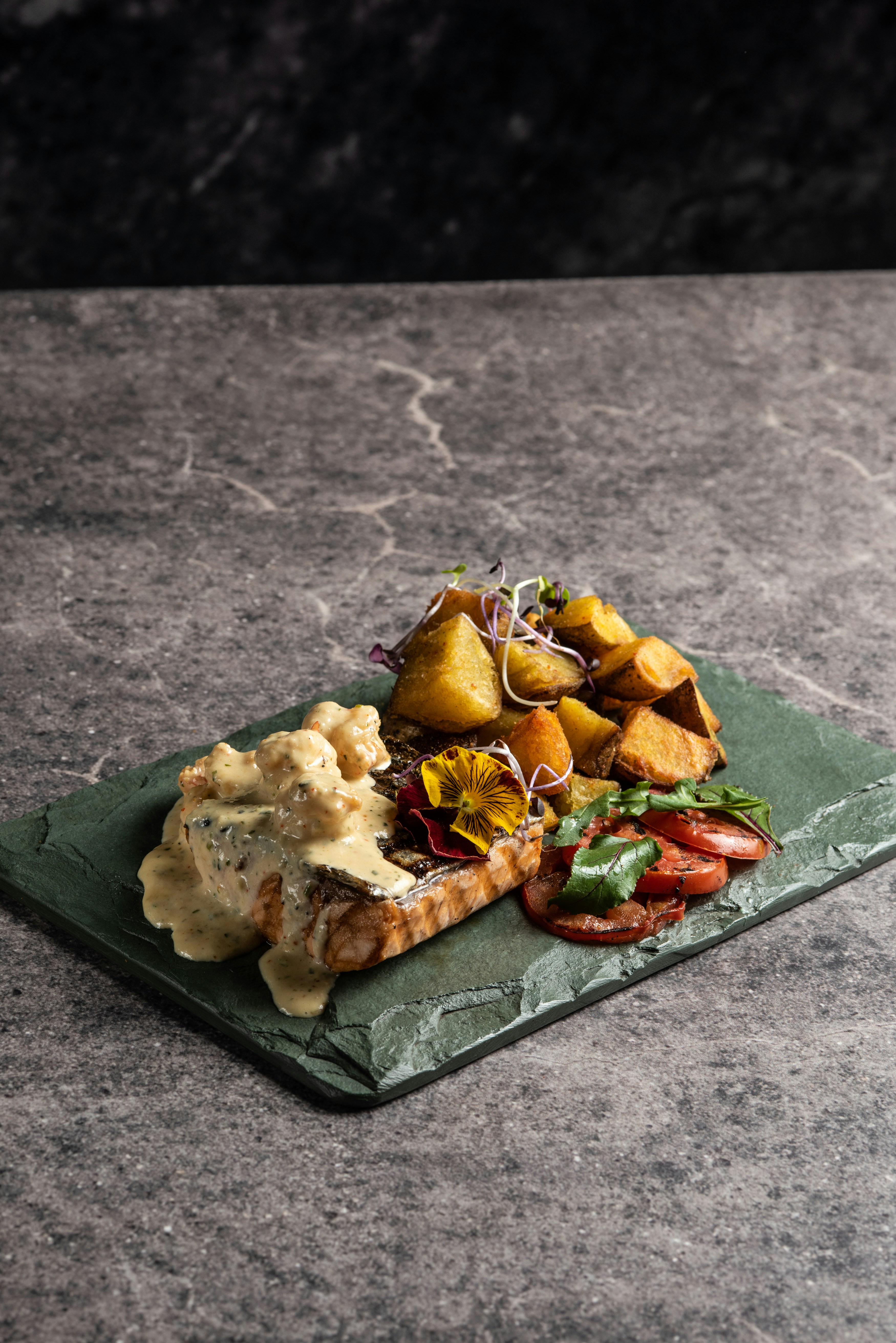 Creamy-topped salmon on slate with herb potatoes and tomato medley
