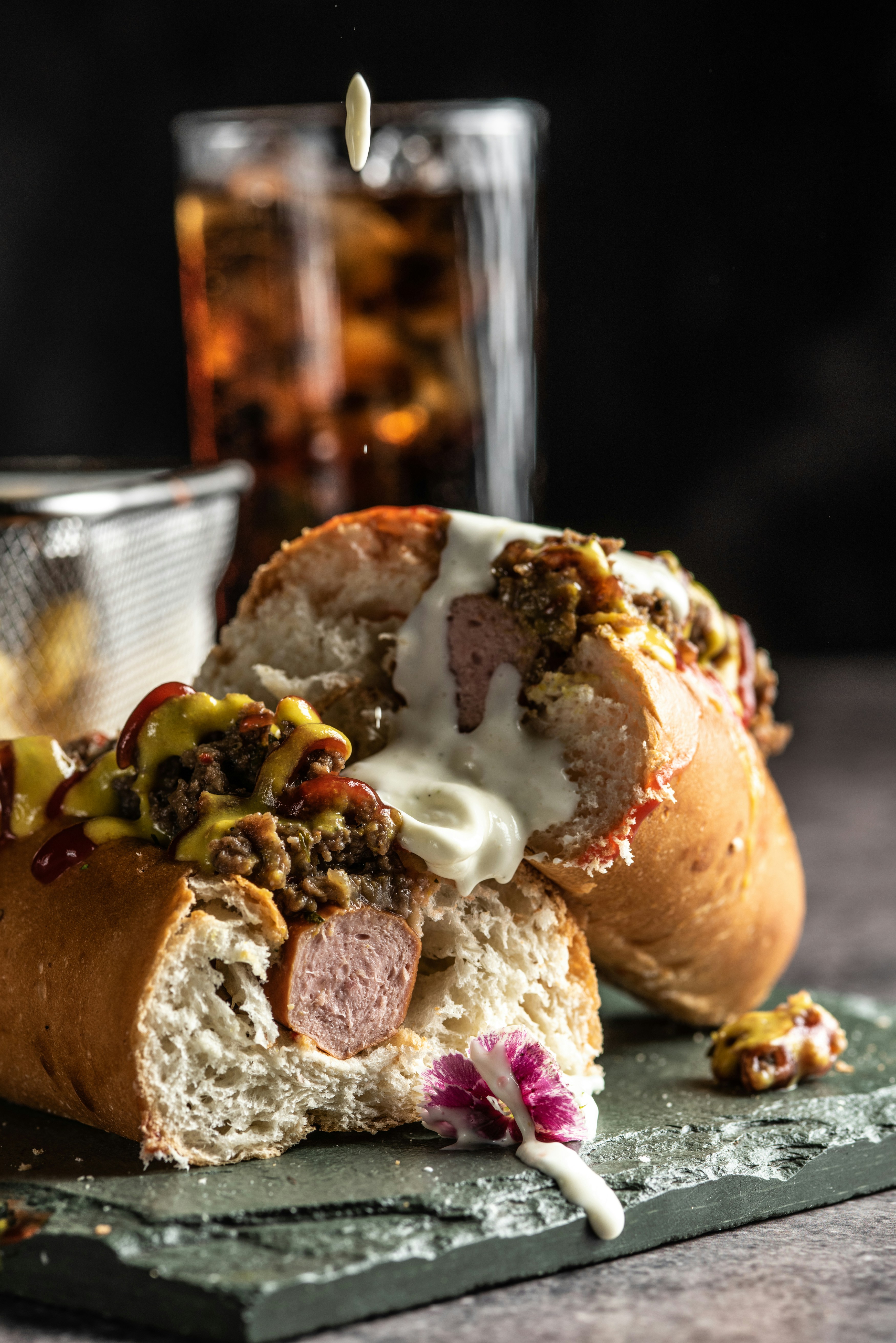 Loaded Gourmet Sausage Bun with Drizzled Toppings on a Slate
