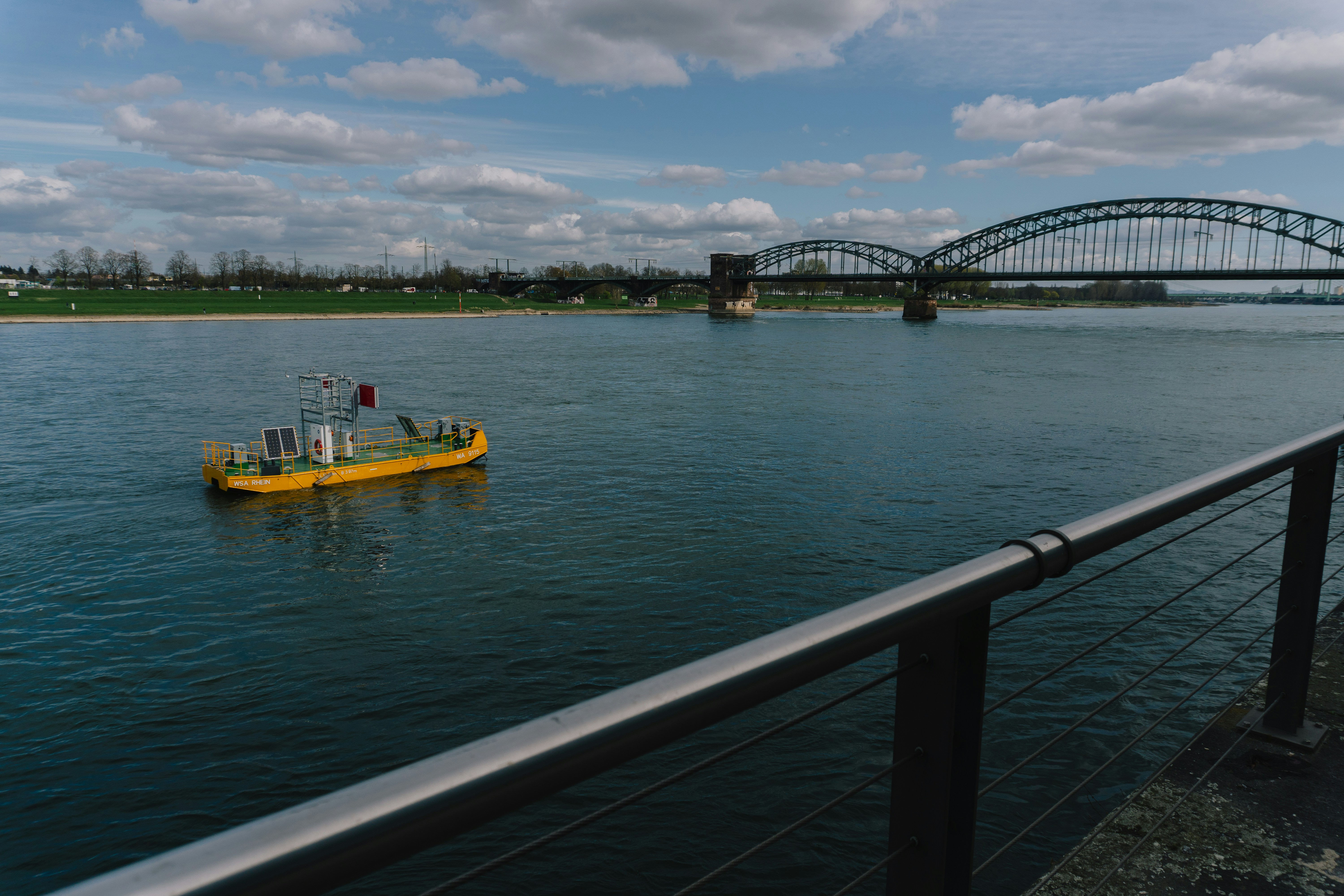 Yellow Work Boat on a Wide River Under a Steel-Arch Bridge