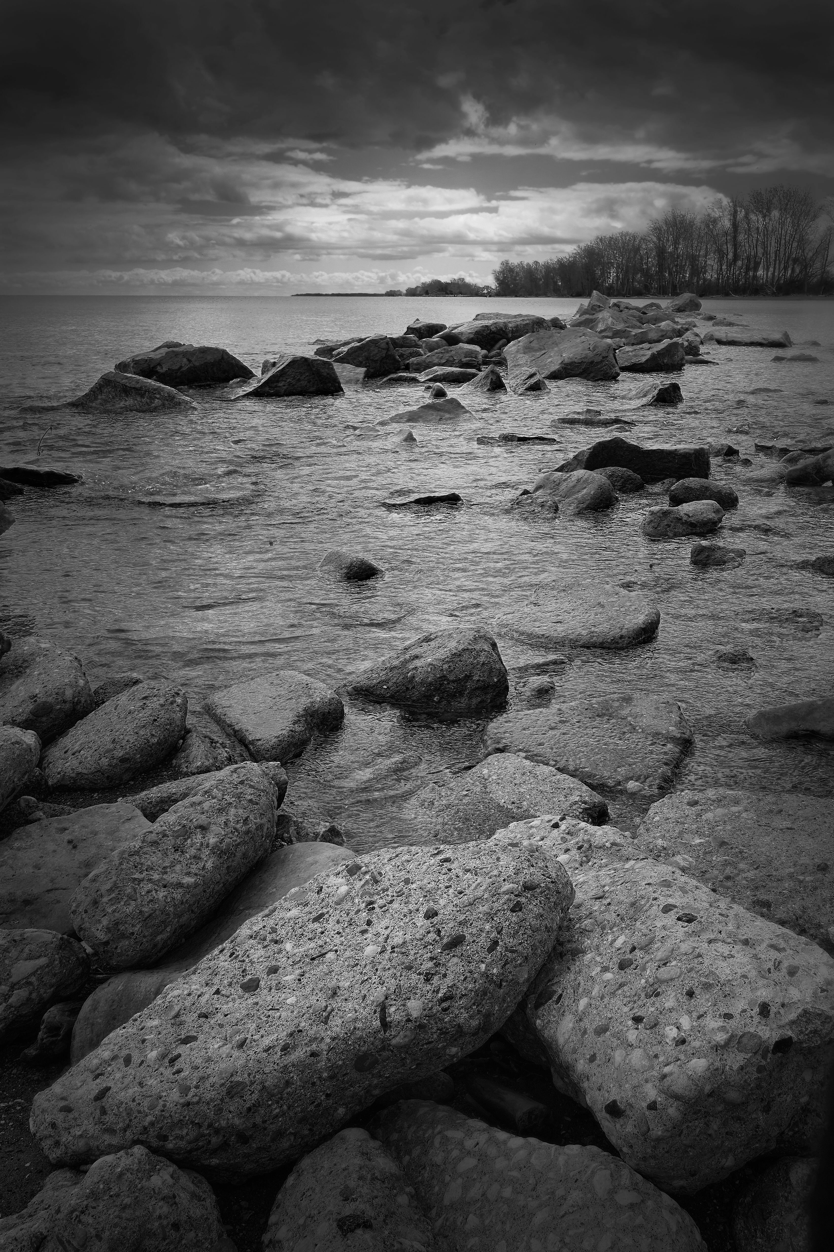 Gravely calm shoreline: weathered rocks stretching toward a distant treeline