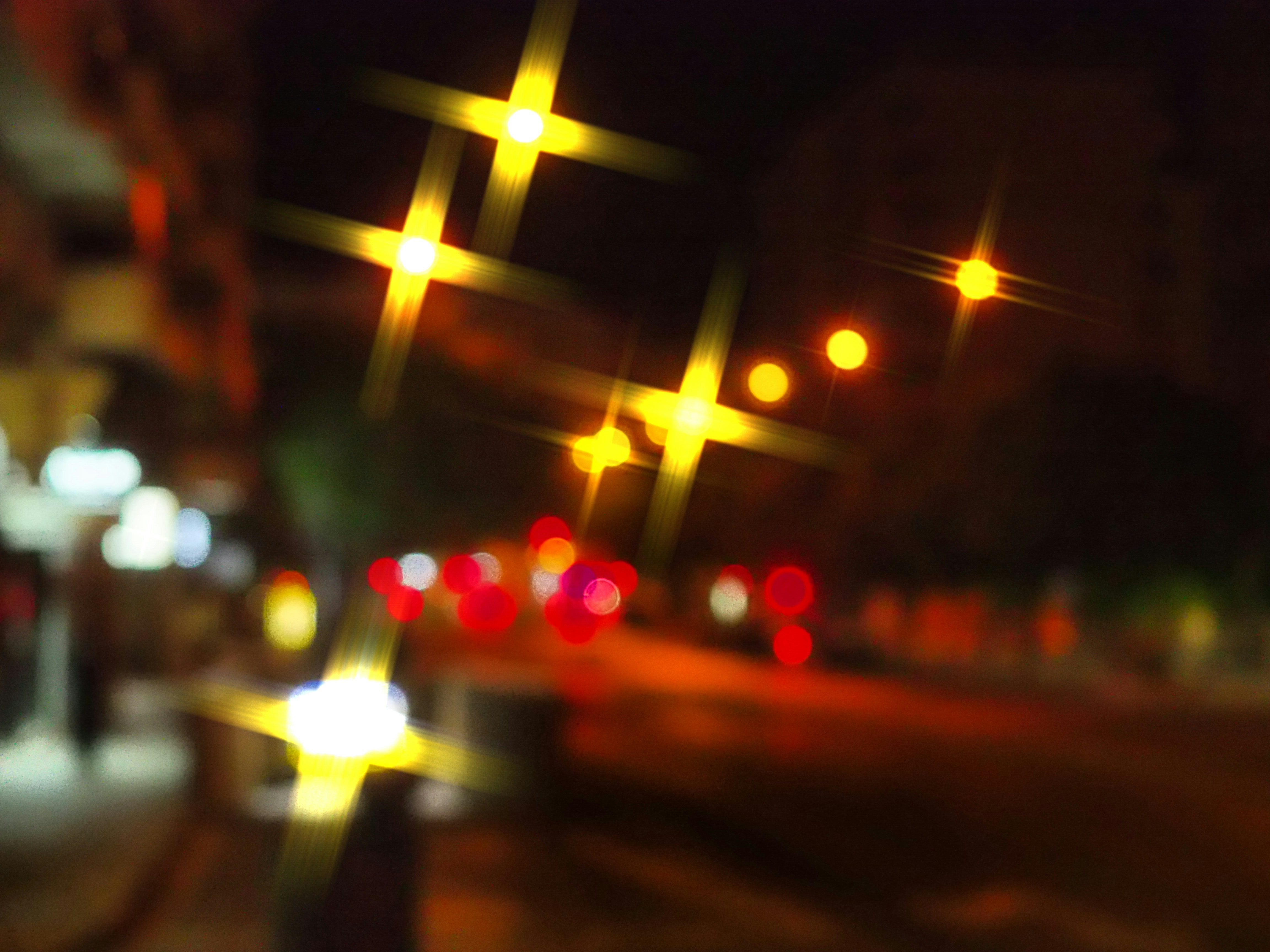 Night street lights glow with starburst bokeh and motion blur, creating an abstract urban vignette. A city scene with warm street lamps rendered as luminous bursts.