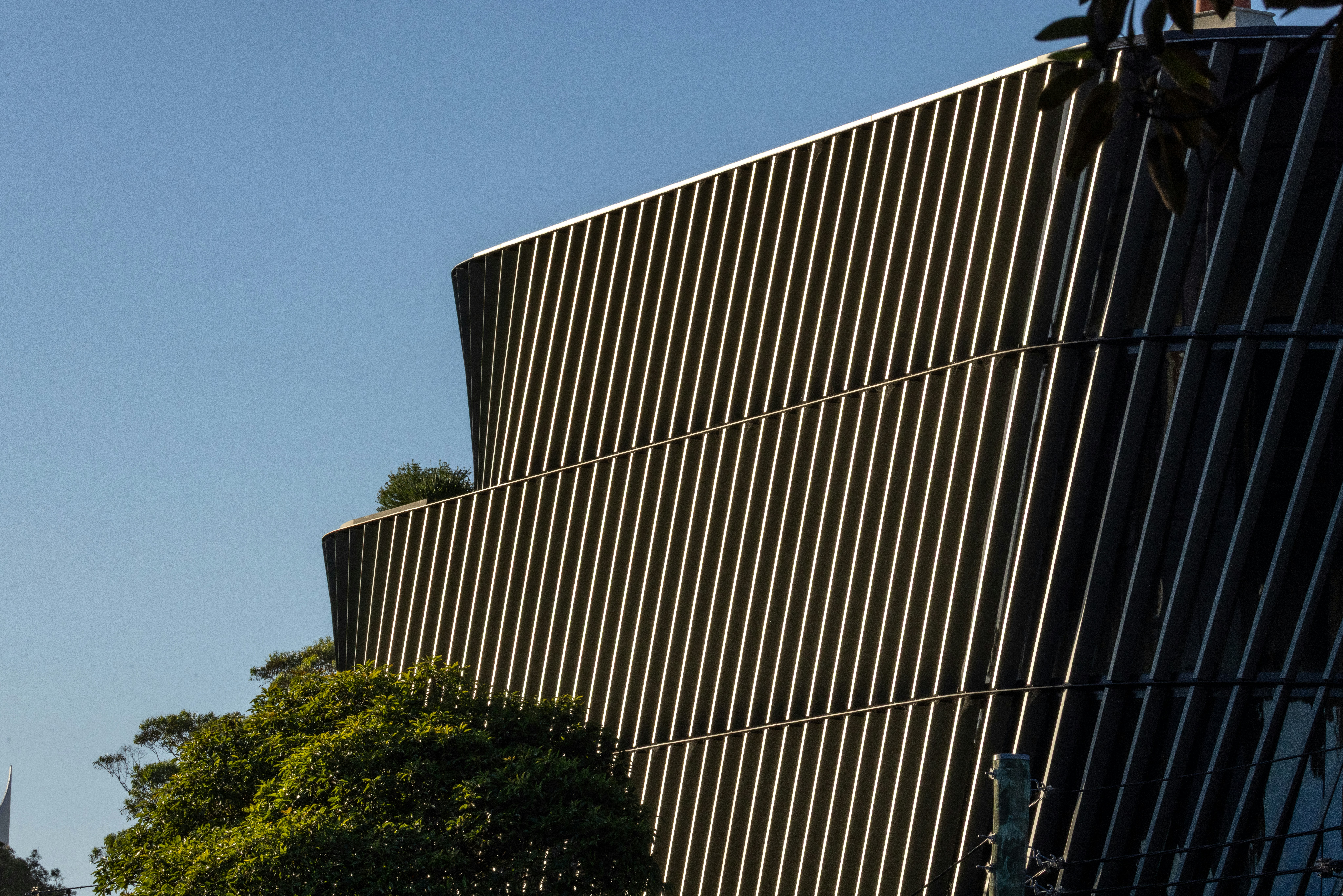 Curved Metal Facade: Striated Modernism Rising Over Greenery