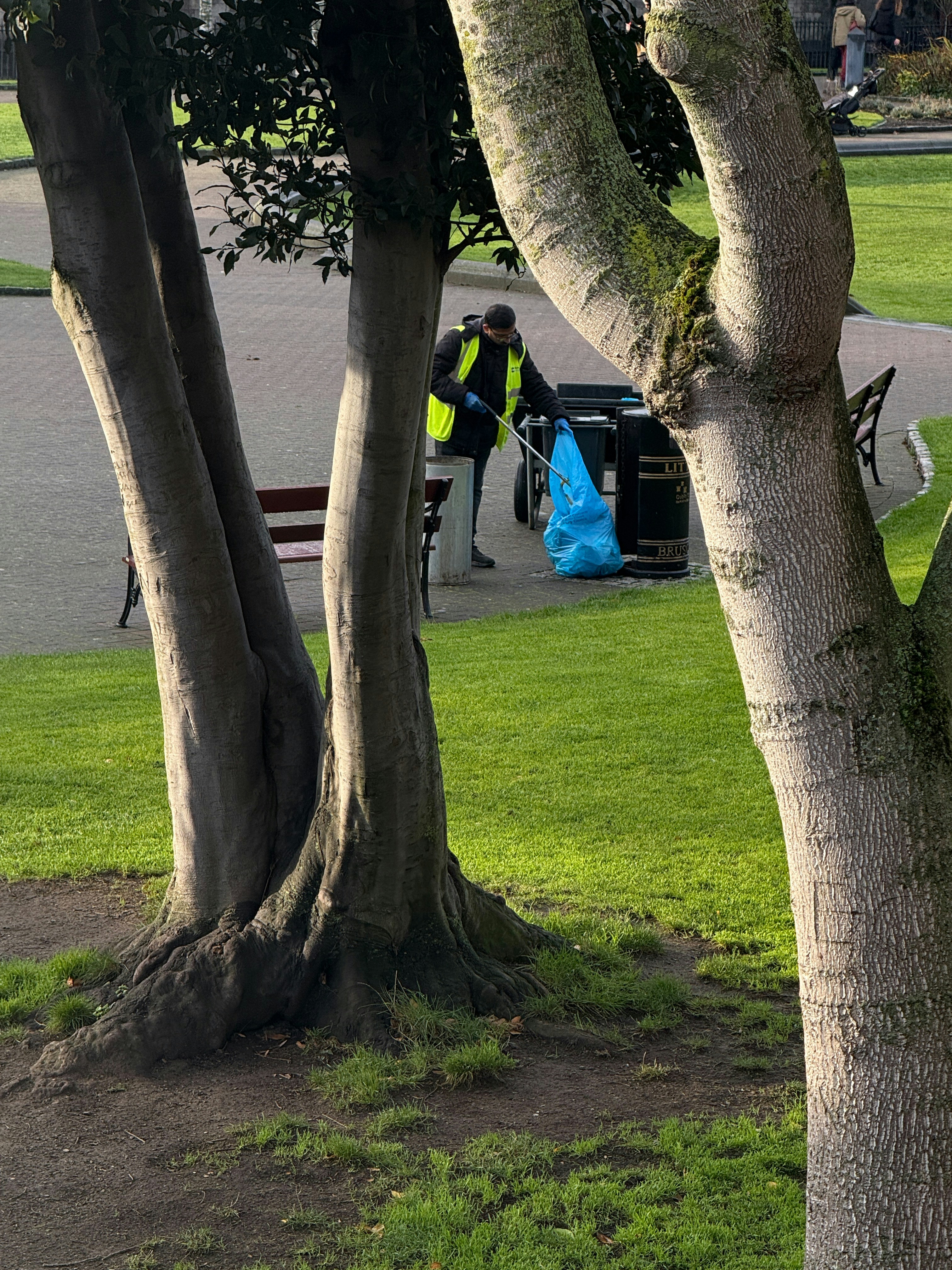 Waste Clean-up in the Park: Worker in High-Visibility Vest Near a Trash Bin