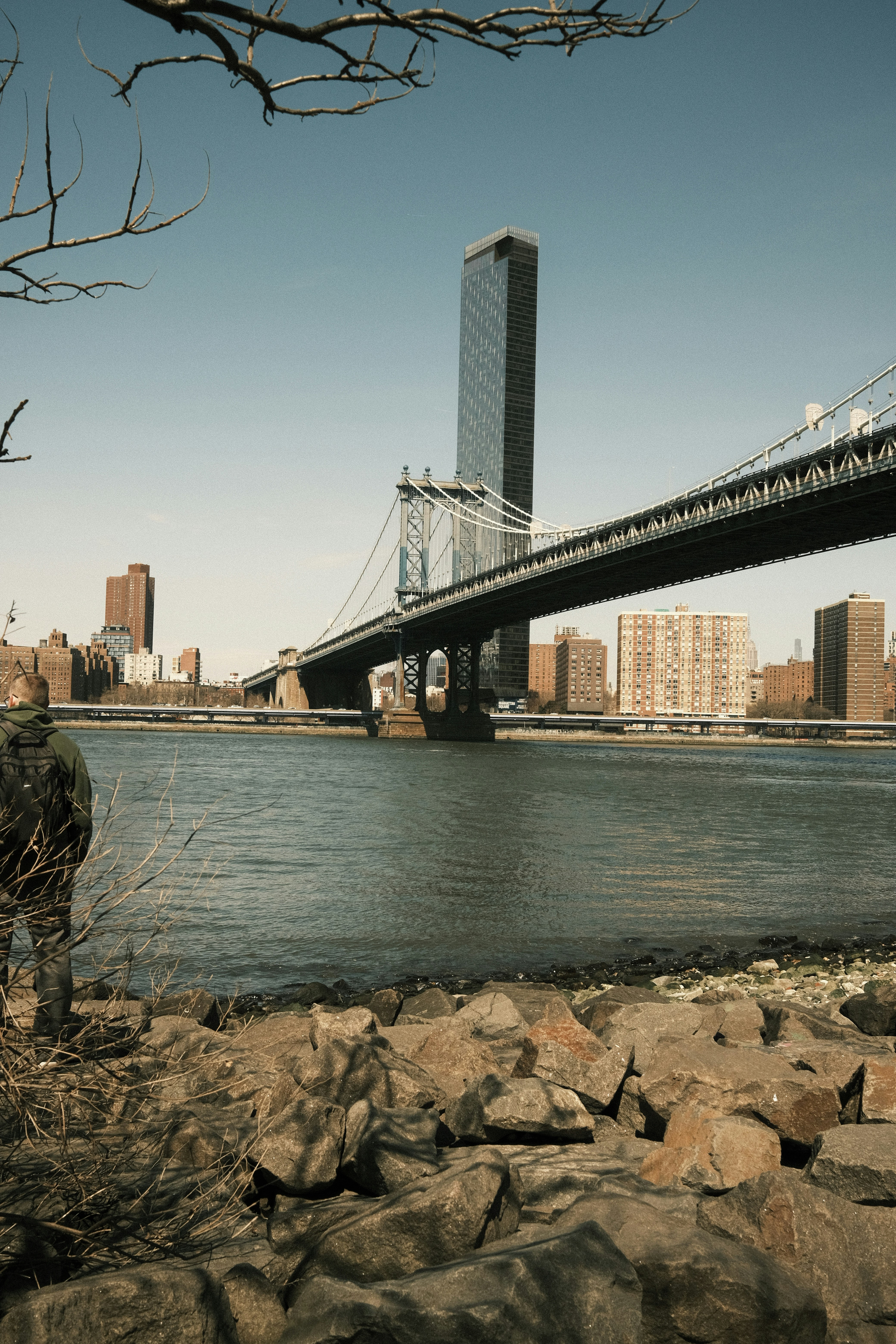 Brooklyn Bridge and skyline: a riverbank vantage with a lone observer