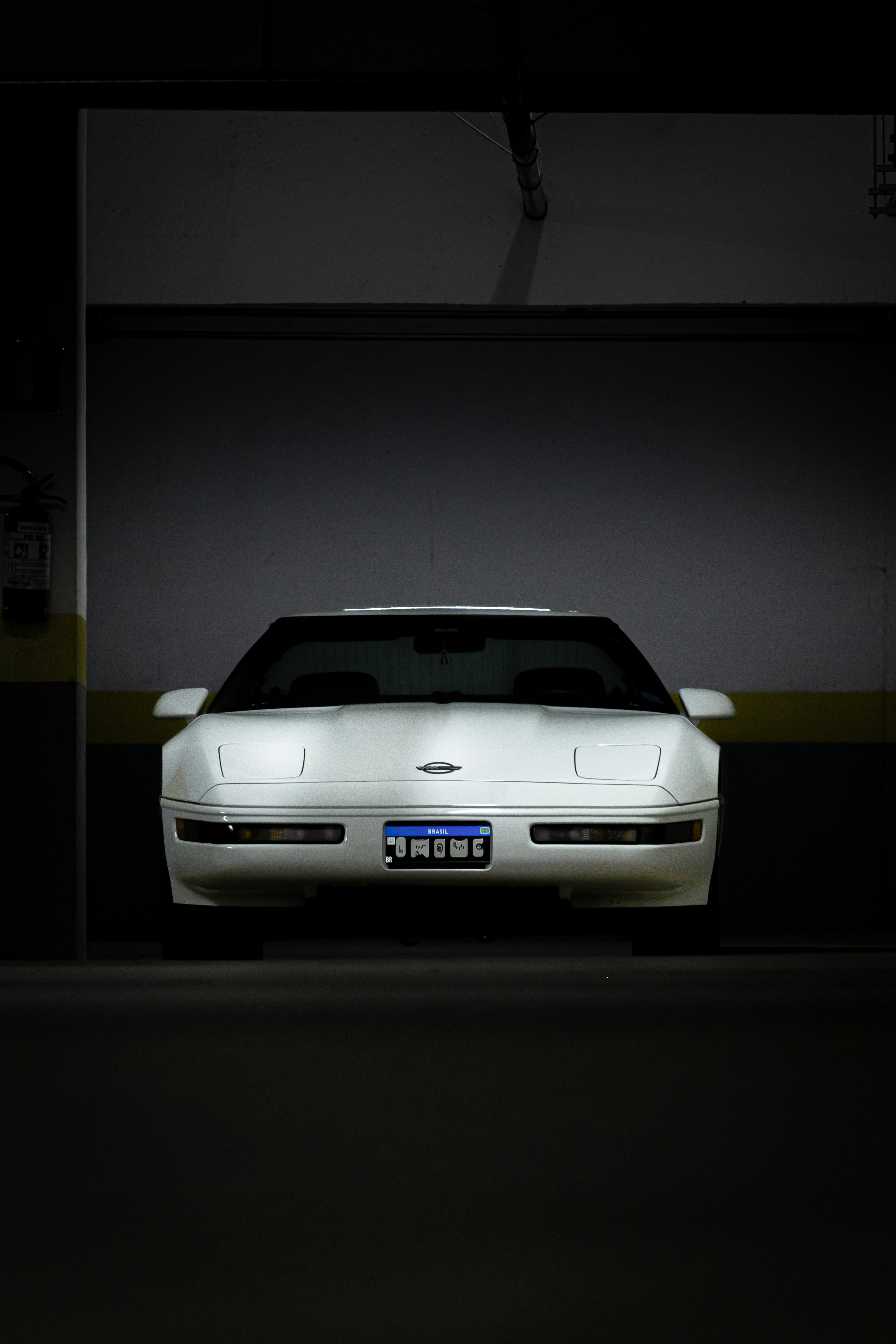 White sports car emerging from the shadows in a dim garage
