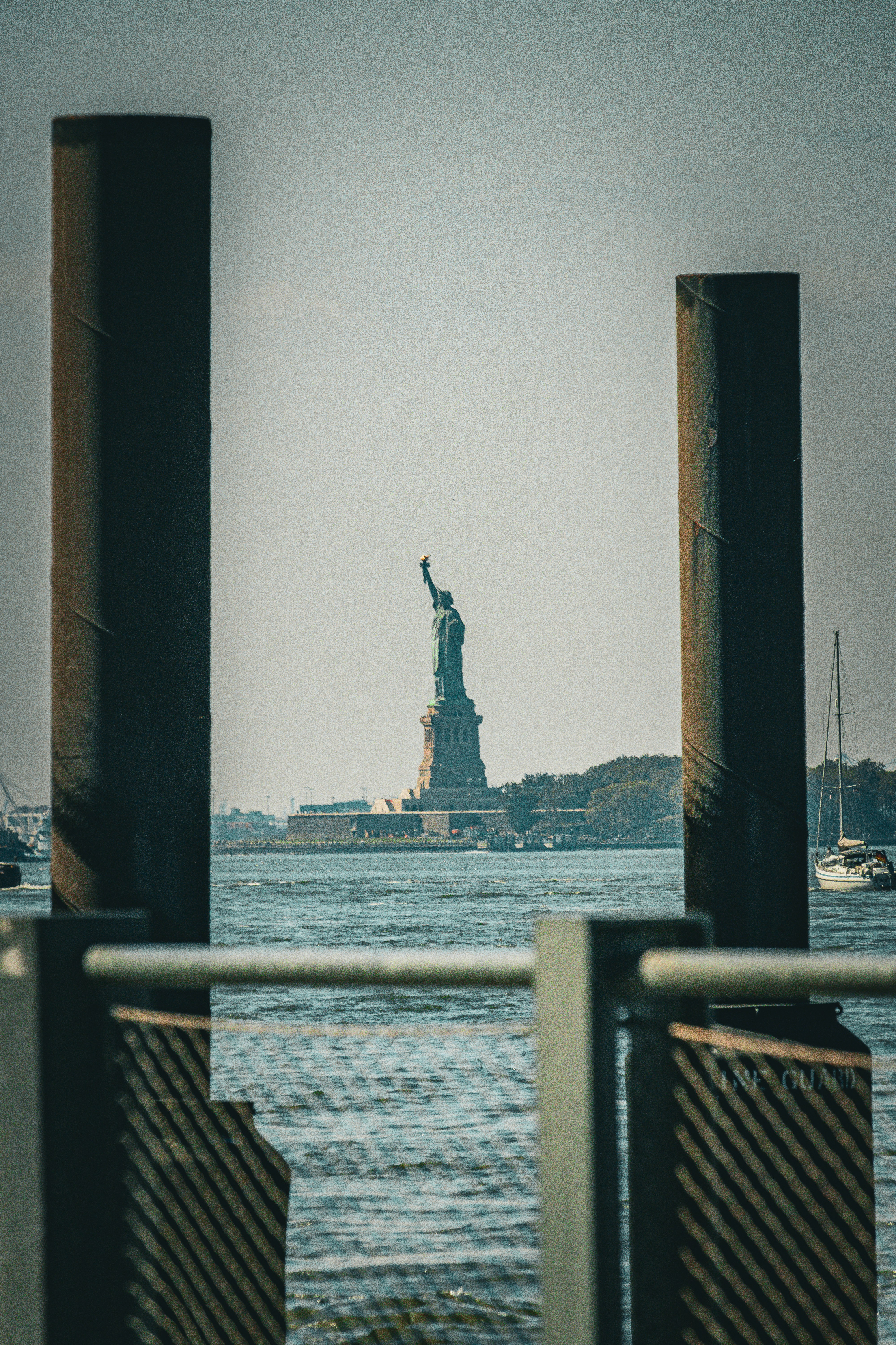 Statue of Liberty framed between weathered piers on a sunlit harbor