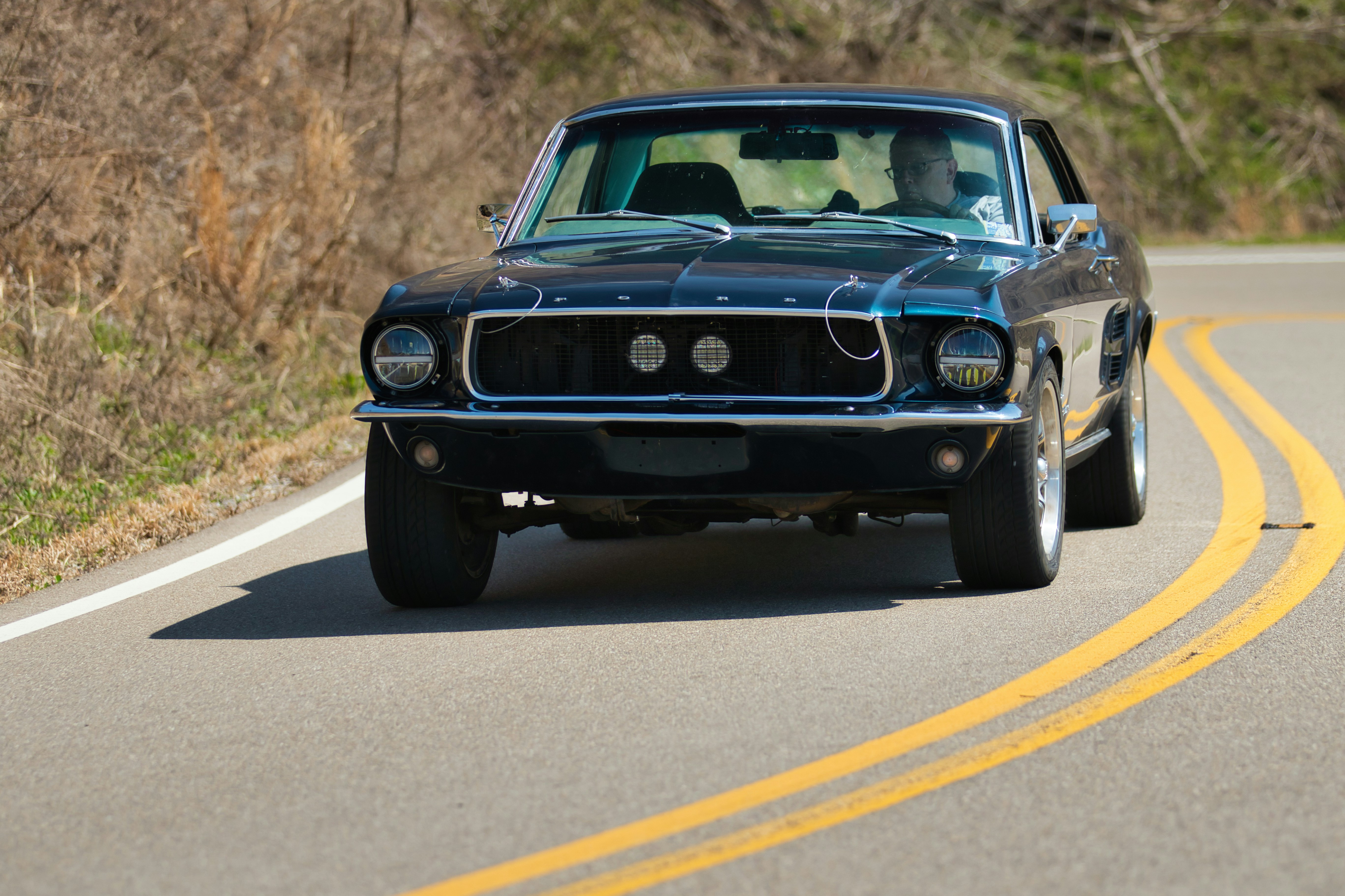 Streetside Classic: A gleaming 1960s Ford Mustang cornering on a sunlit two-lane