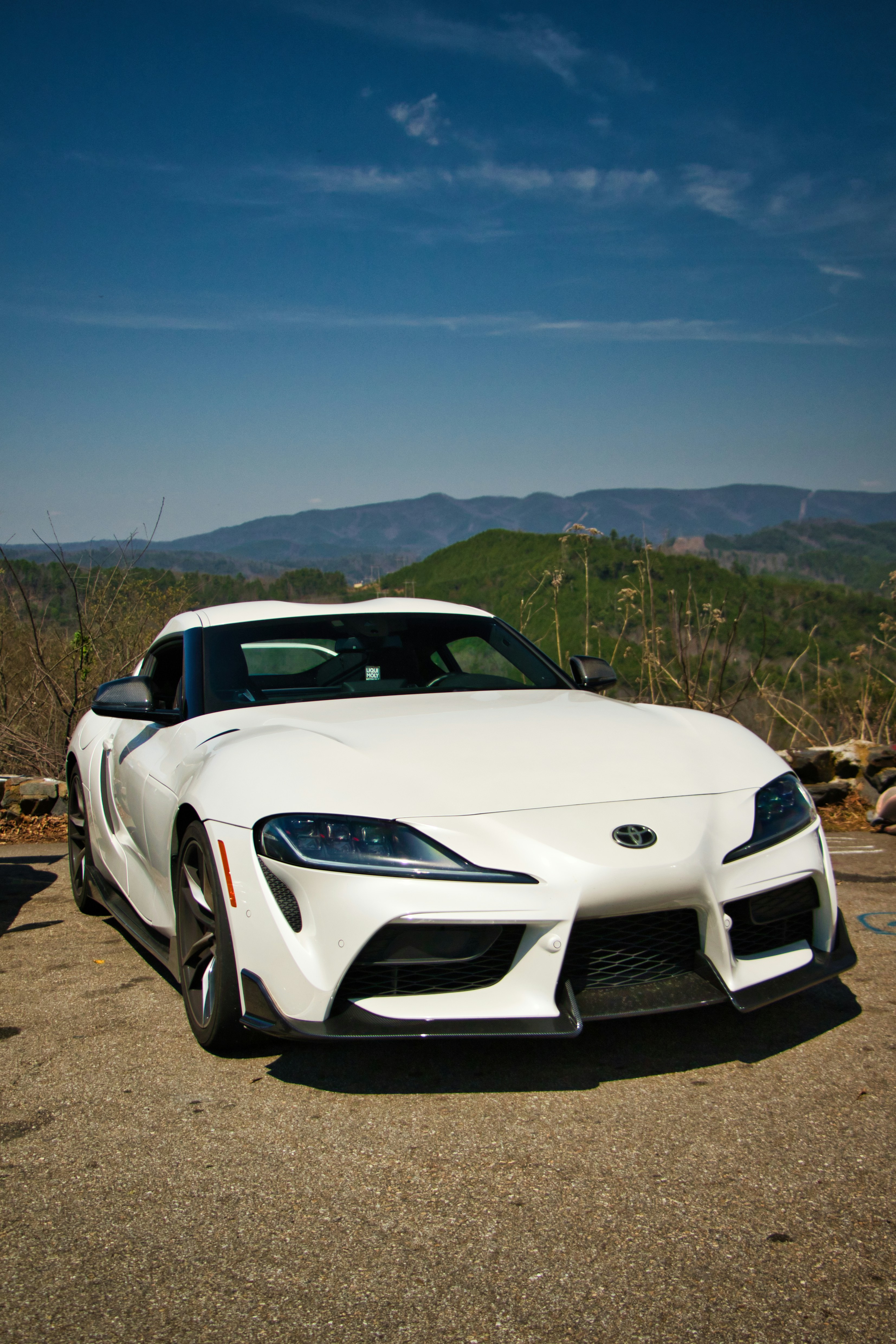 White Toyota sports car under a blue sky with rolling hills