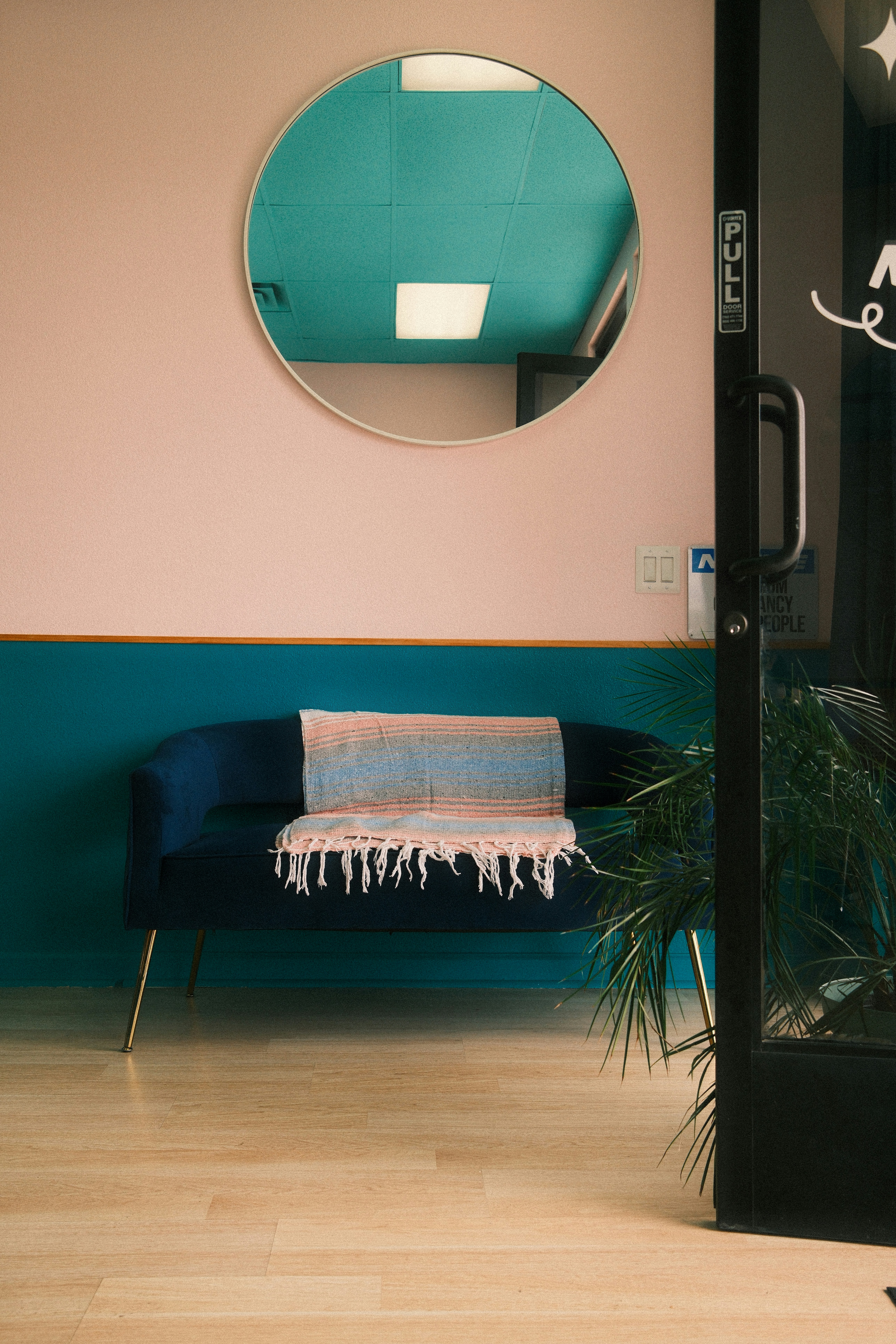 Echo of Color: A Teal Ceiling Reflected in a Round Mirror over a Pink and Teal Sofa