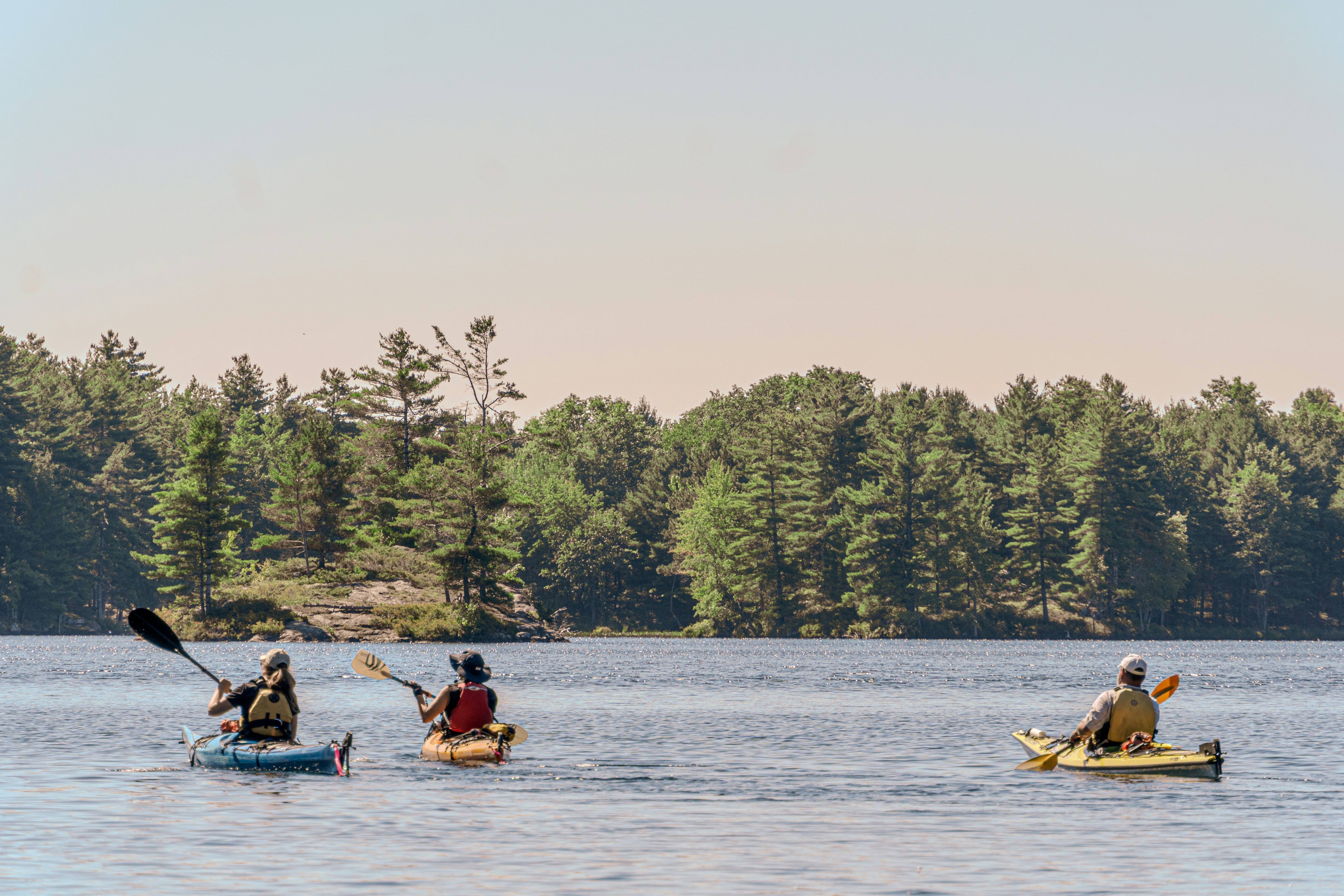 Three Kayaks Slice Through a Calm Lake at Dusk