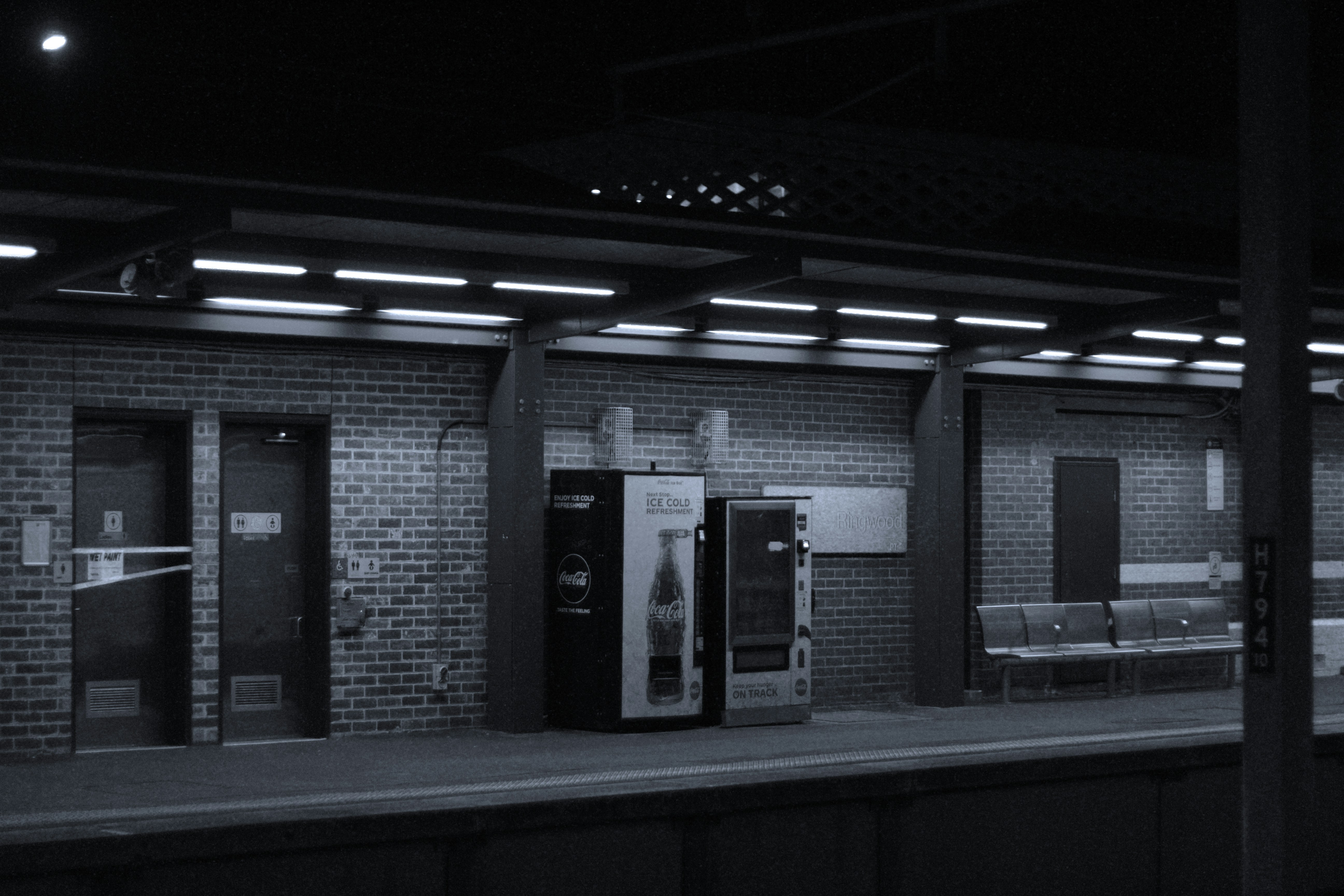  dim, monochrome-subdued subway platform with vending machines and benches in a quiet station.