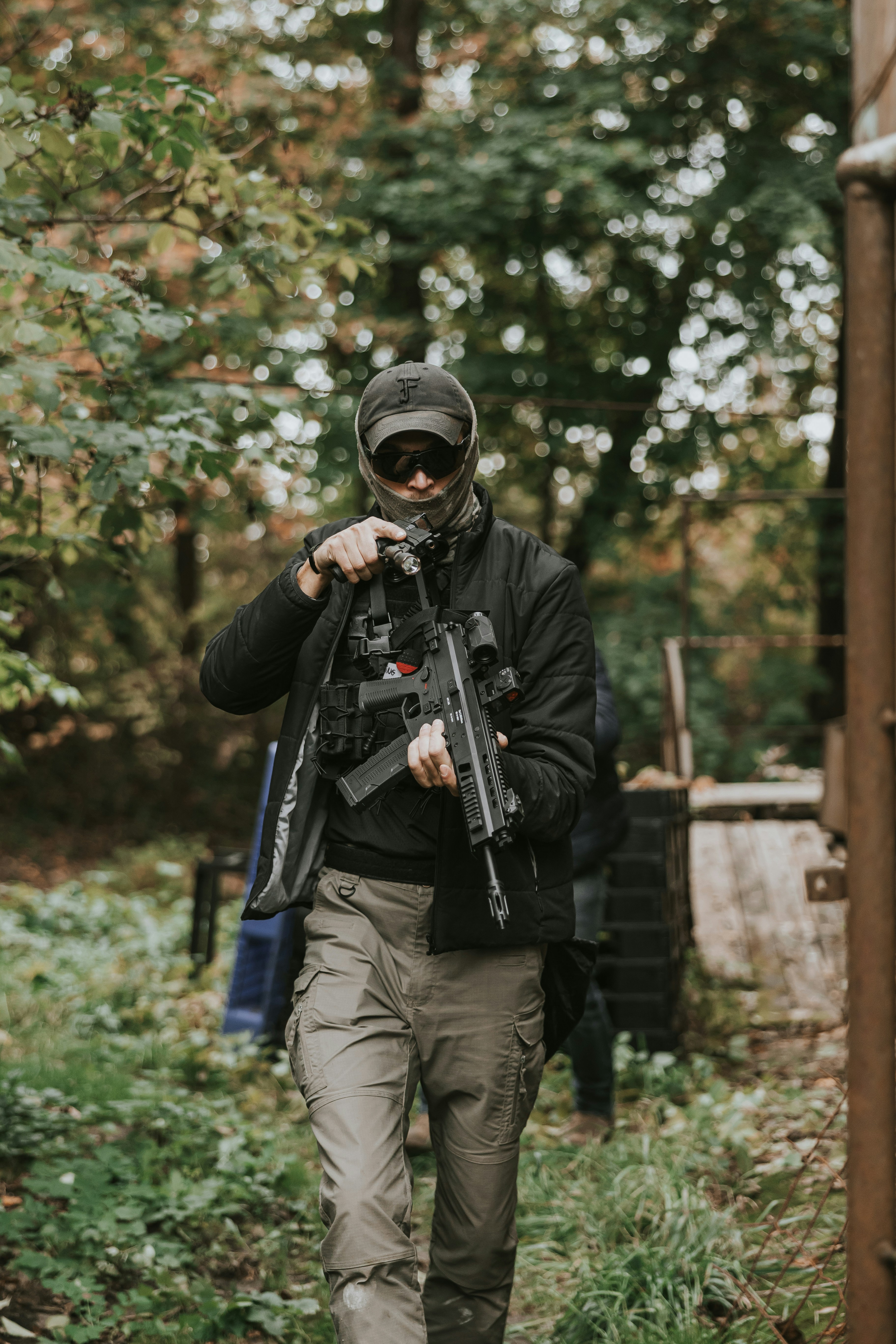 Masked operator strides through autumn brush with a tactical rifle