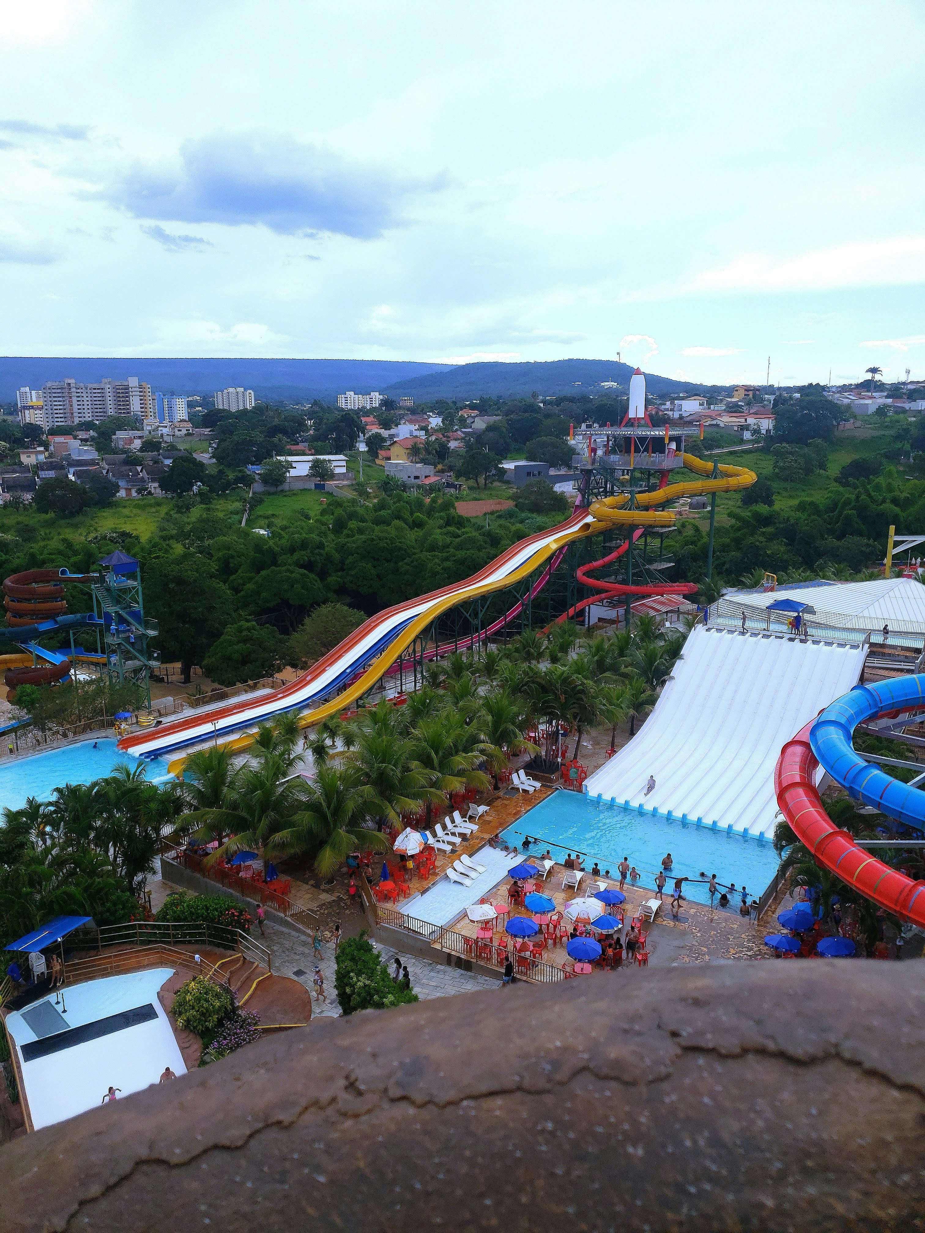 Aerial View of a Sunlit Water Park with Spiraling Slides and Poolside Activity