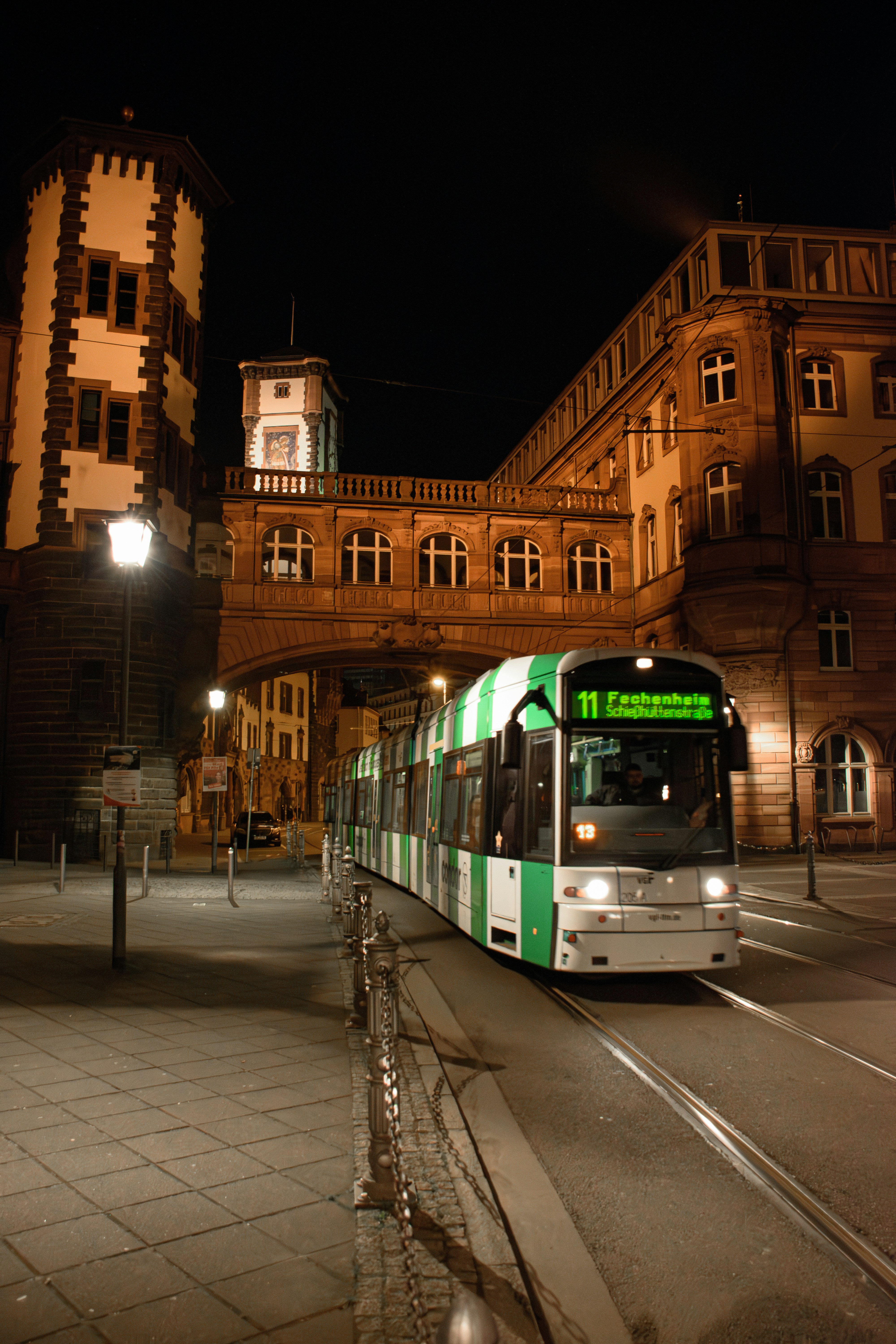 Night tram at the archway: warm street glow meets green urban transit