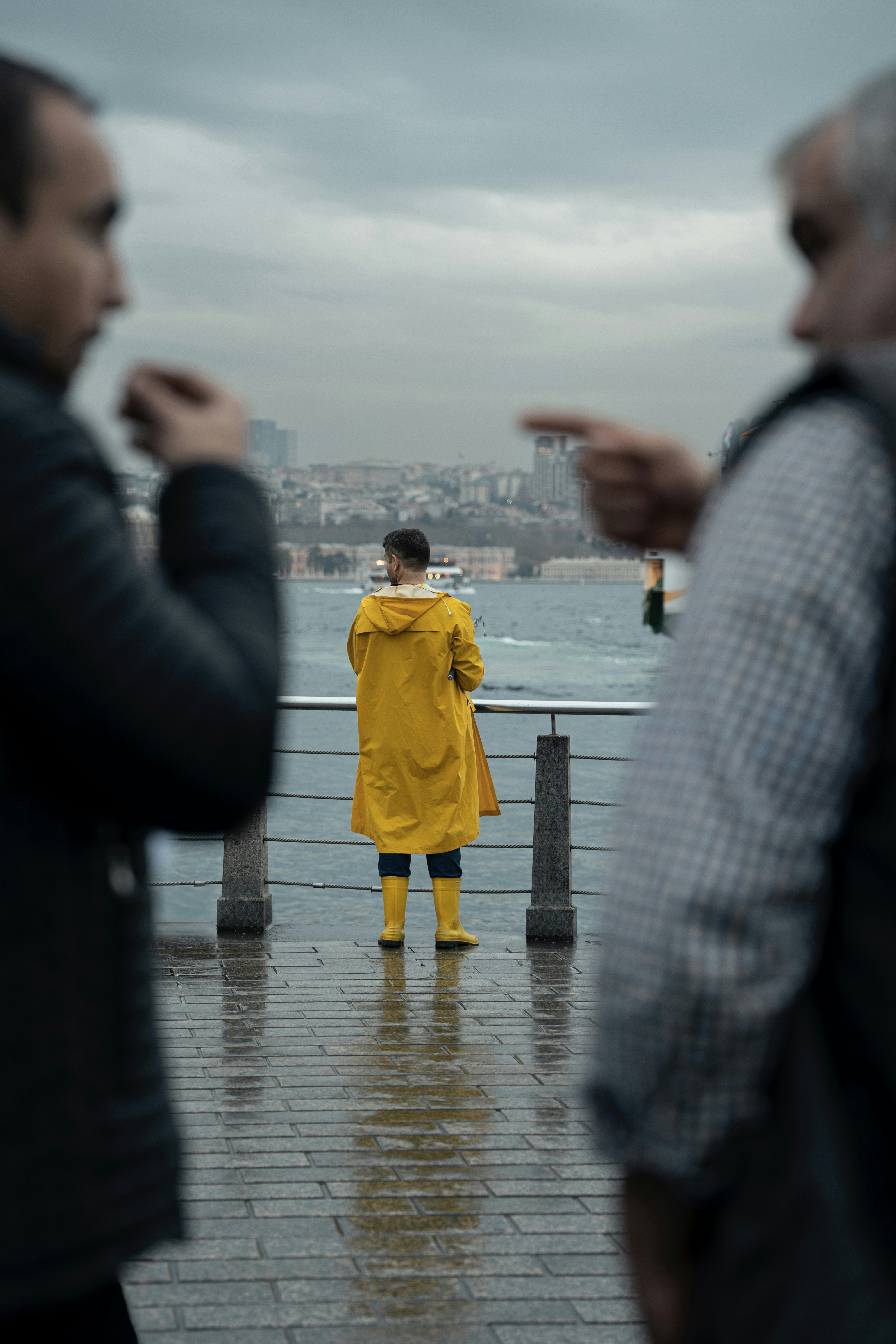 Yellow raincoat at the quay: a solitary figure framed by moving silhouettes
